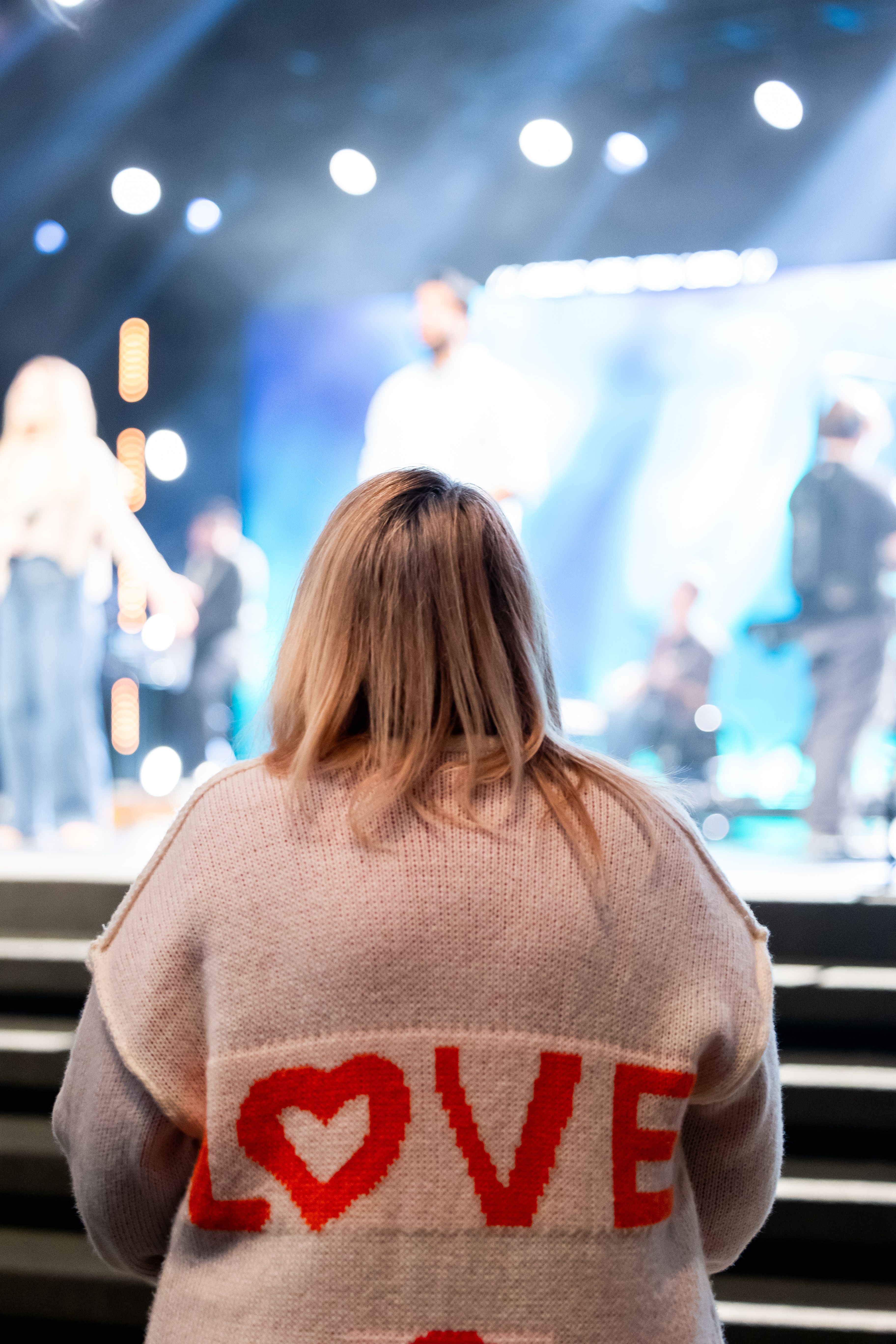 Woman in 'Love' Sweater Observing Stage Performance · Free Stock Photo