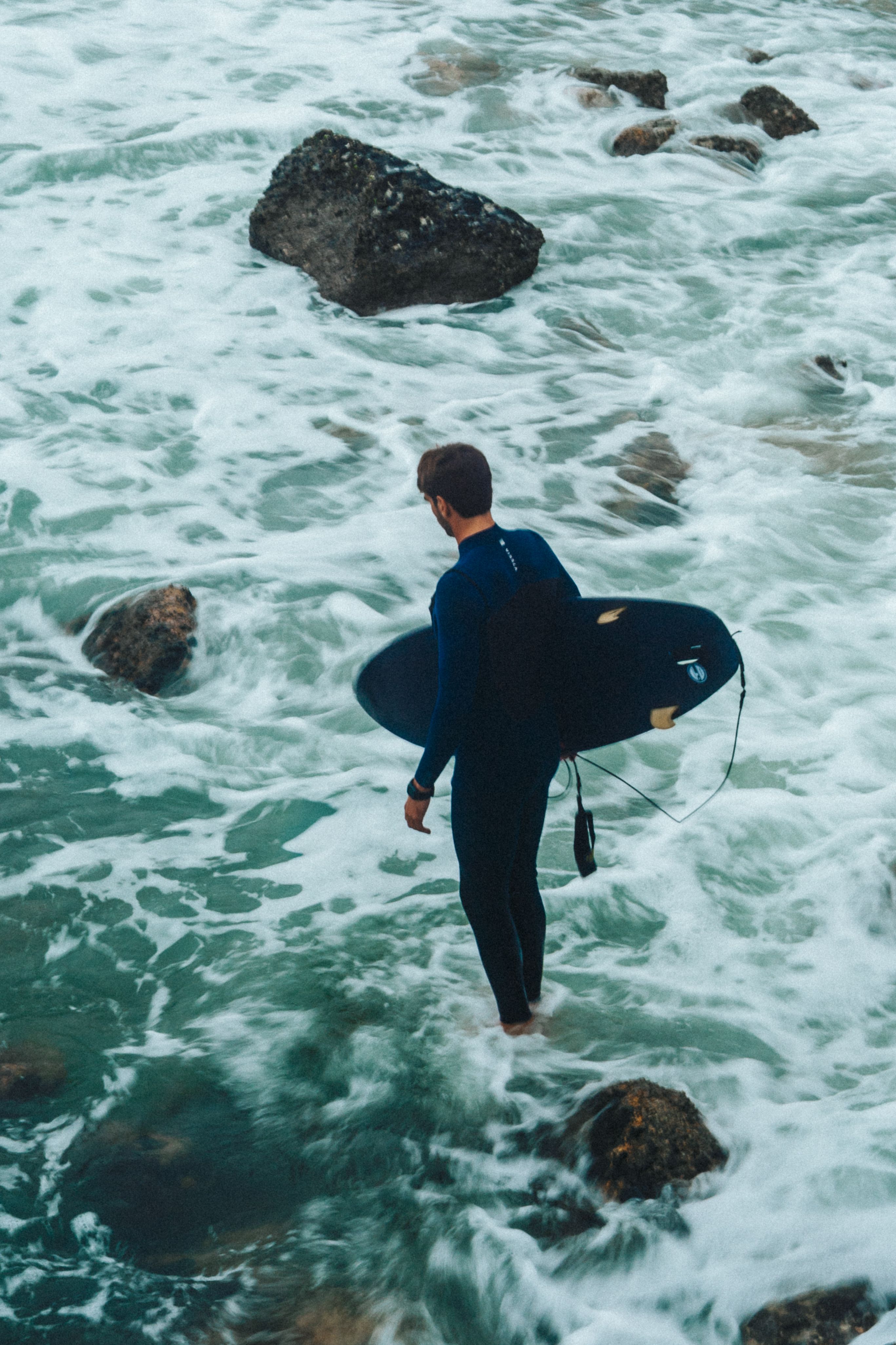 Surfer Navigating Rocky Shoreline in Wetsuit · Free Stock Photo