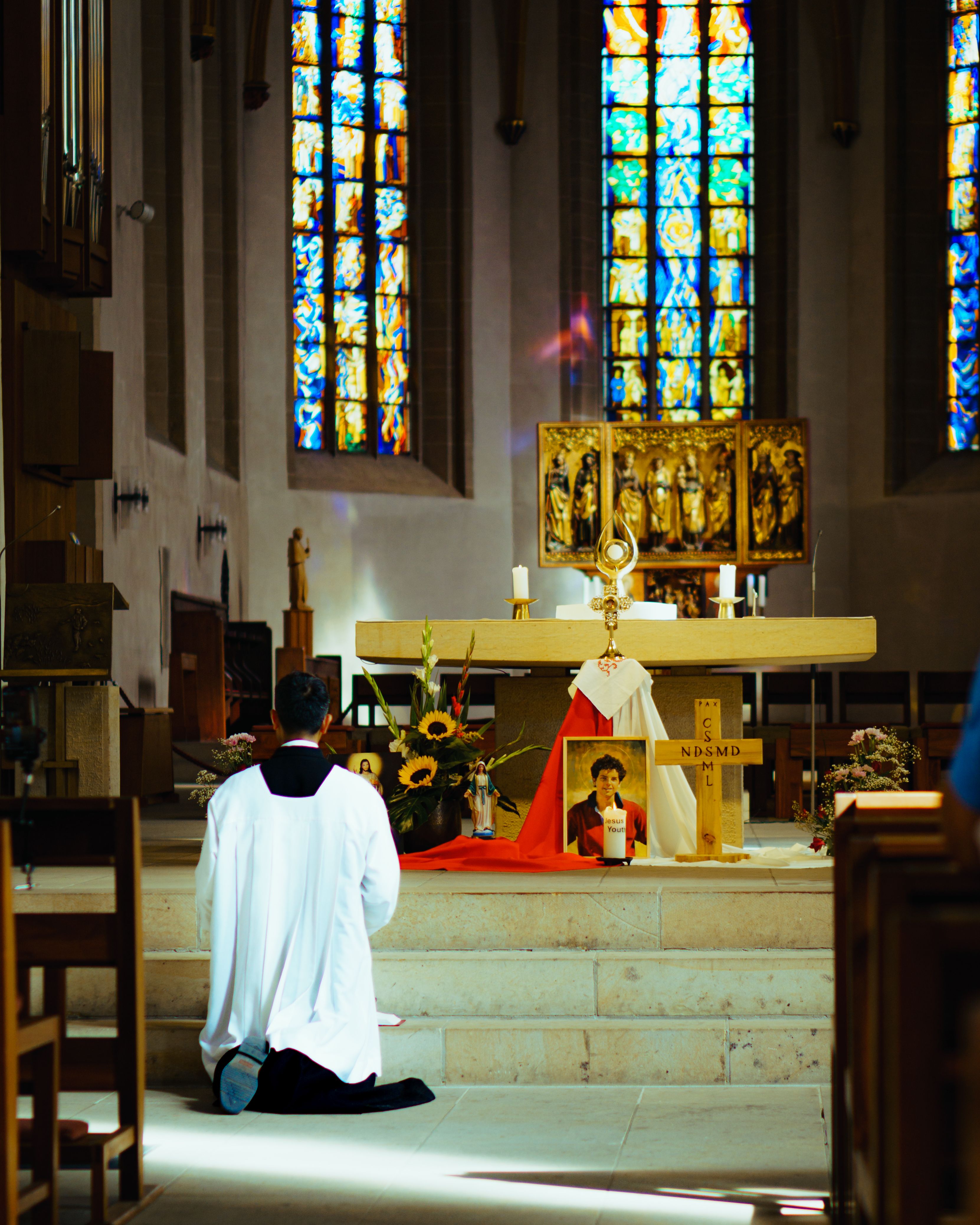 Priest Kneeling in Historic Church with Stained Glass · Free Stock Photo