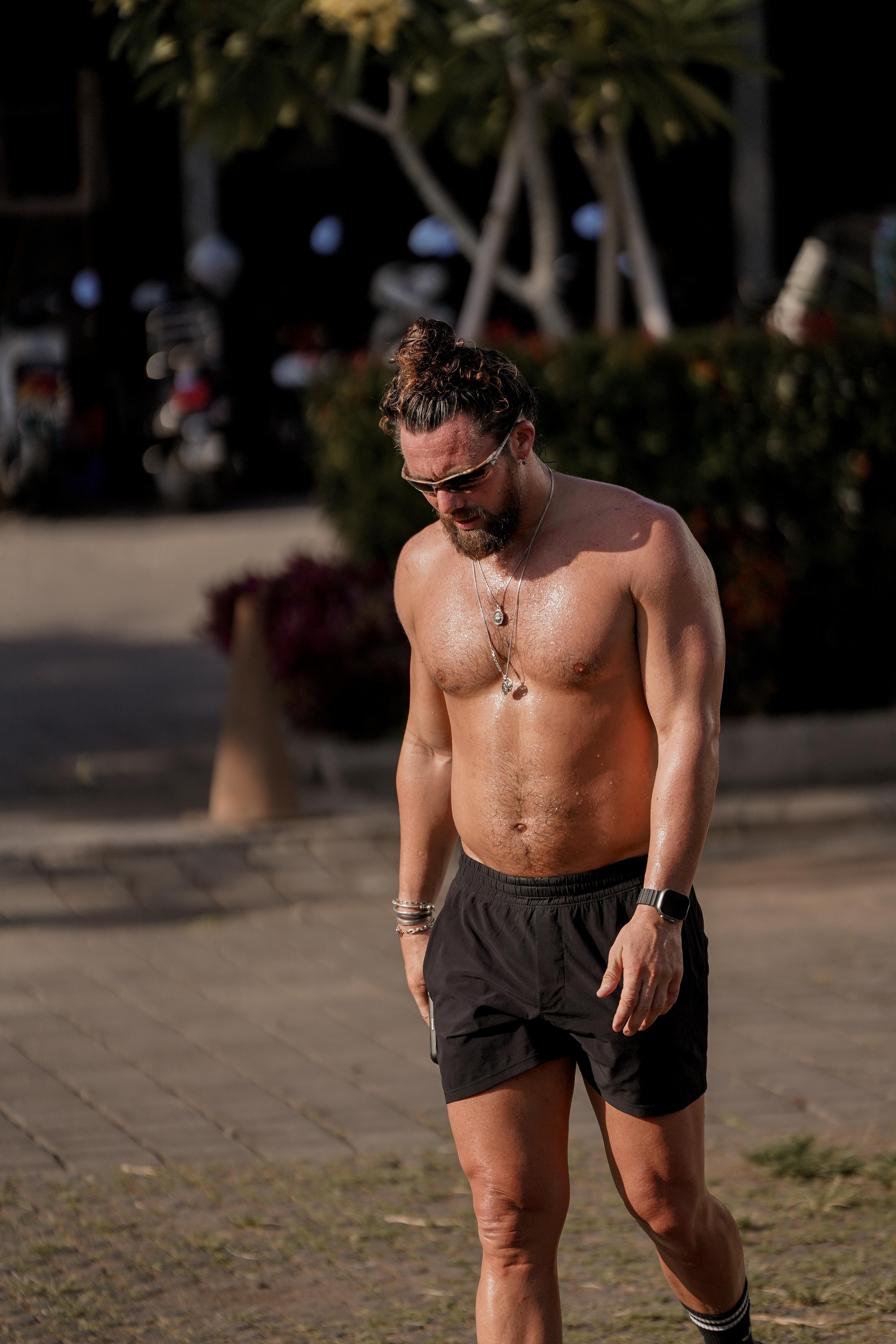 Shirtless Man Walking Outdoors in Sunny Urban Area · Free Stock Photo
