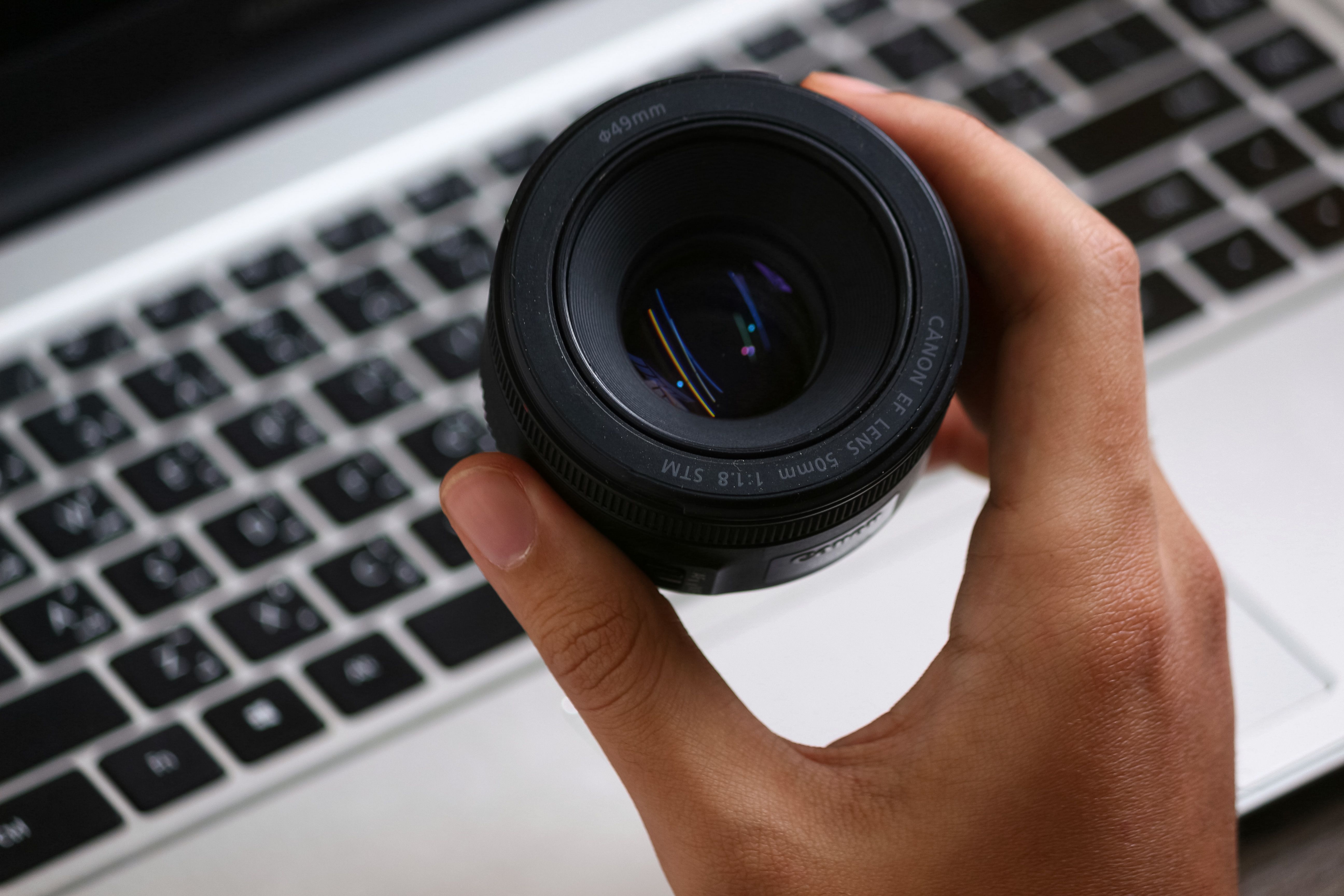 Close-up of Hand Holding DSLR Lens Over Laptop · Free Stock Photo