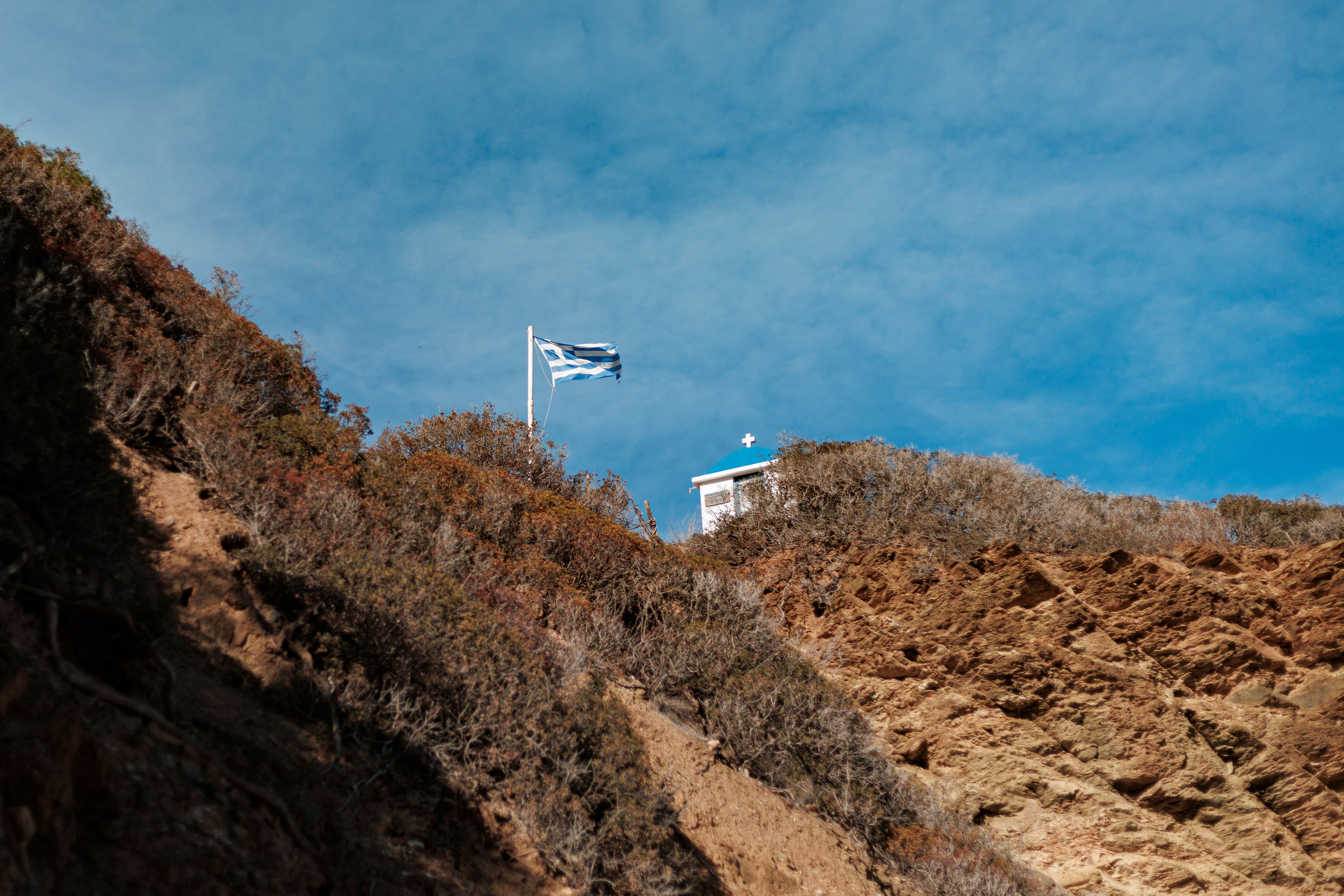 Greek Chapel and Flag on Rocky Cliffside · Free Stock Photo