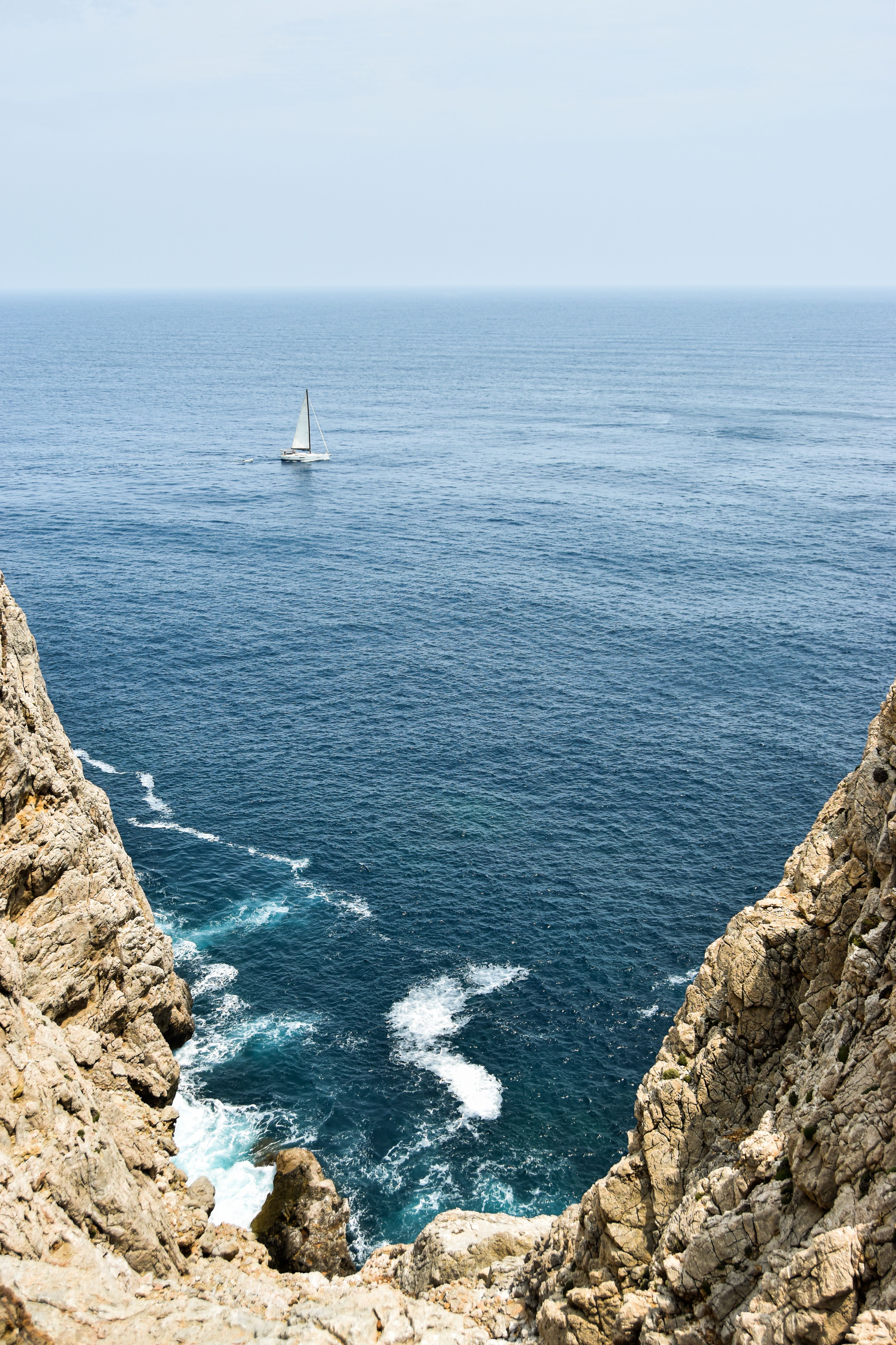 Sailboat on a Vast Ocean Seen from a Rocky Cliff · Free Stock Photo