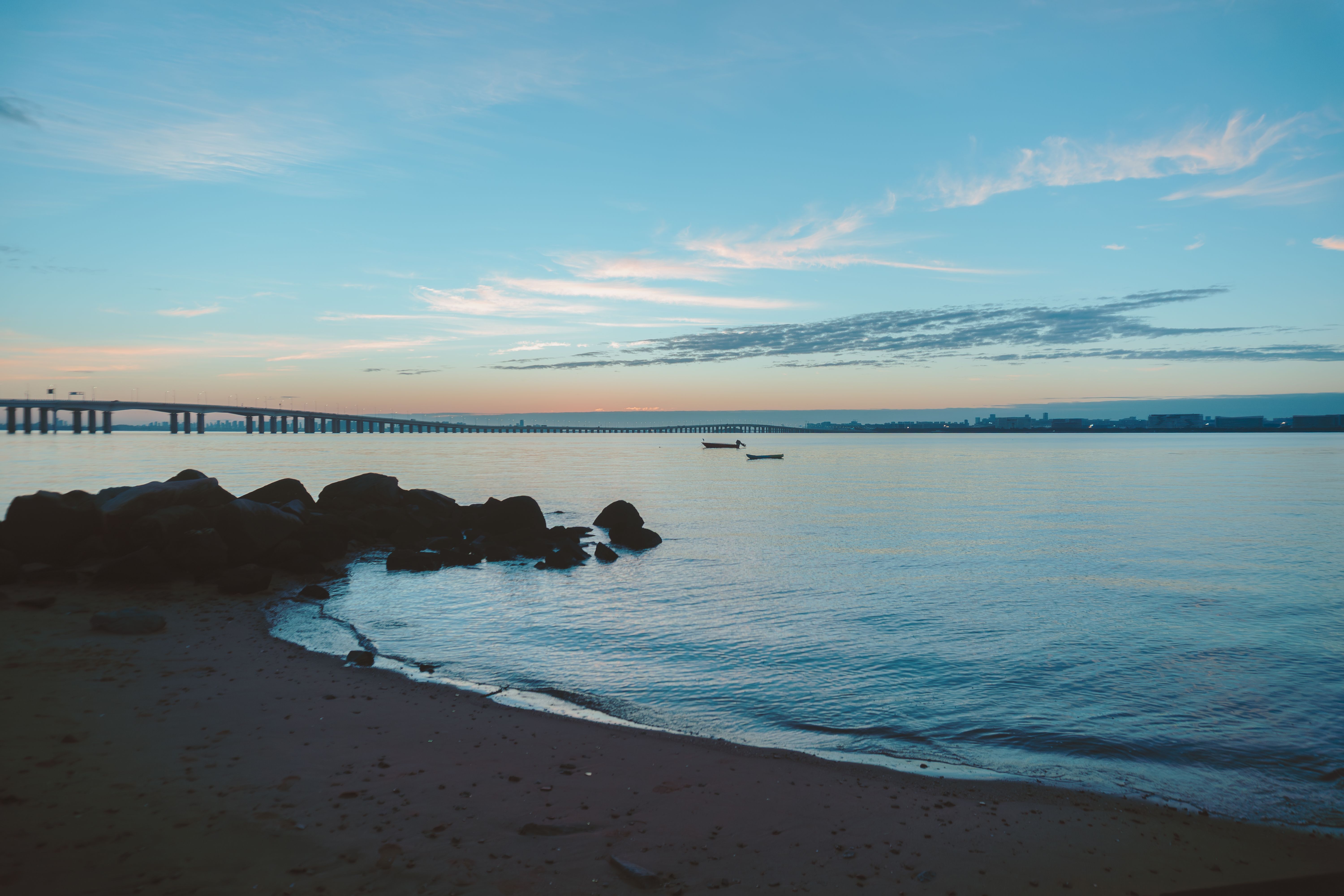 Scenic Beach Sunset with Calm Waters and Bridge · Free Stock Photo