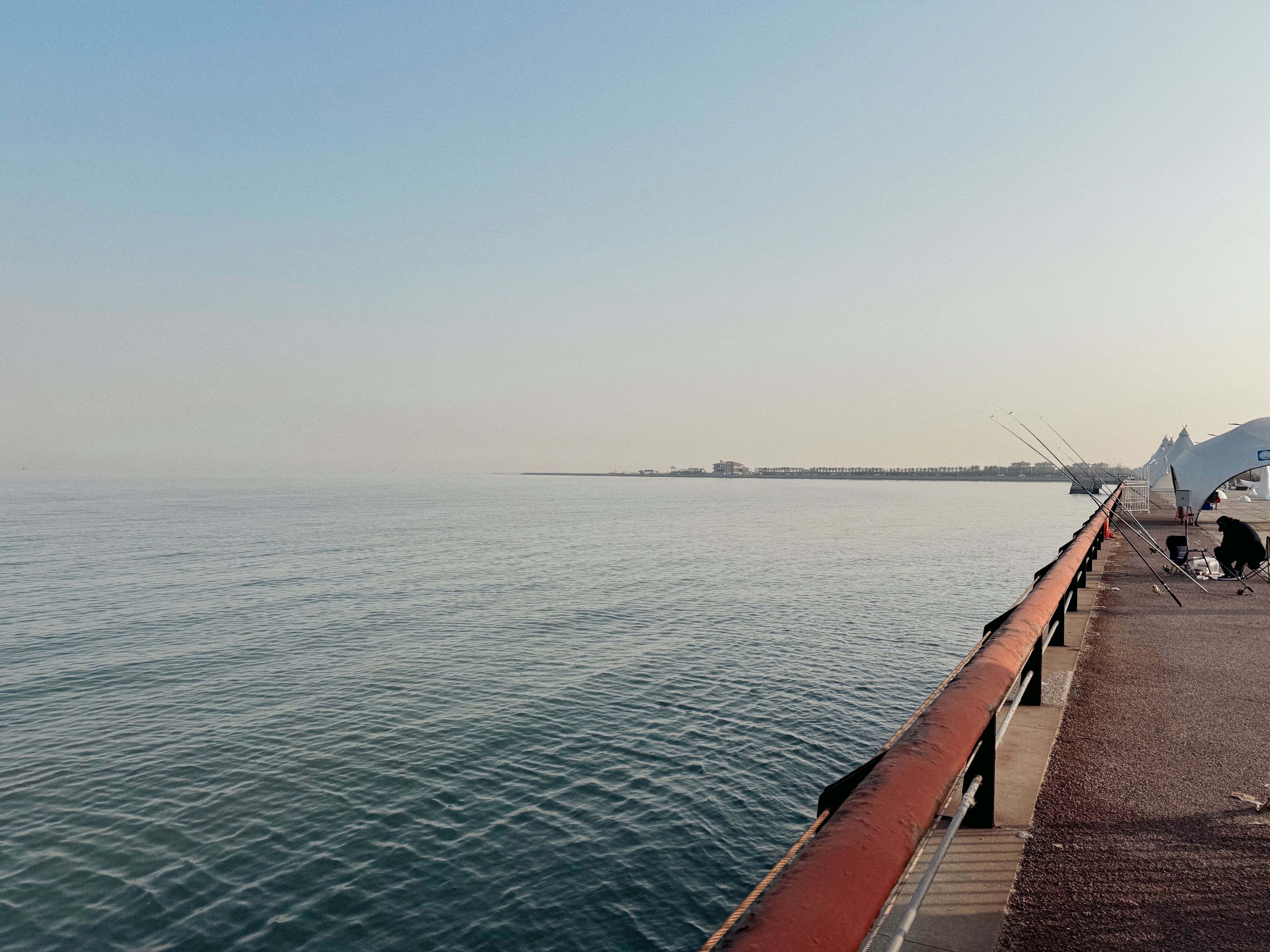Peaceful Waterfront Walkway with Fishing Rods · Free Stock Photo