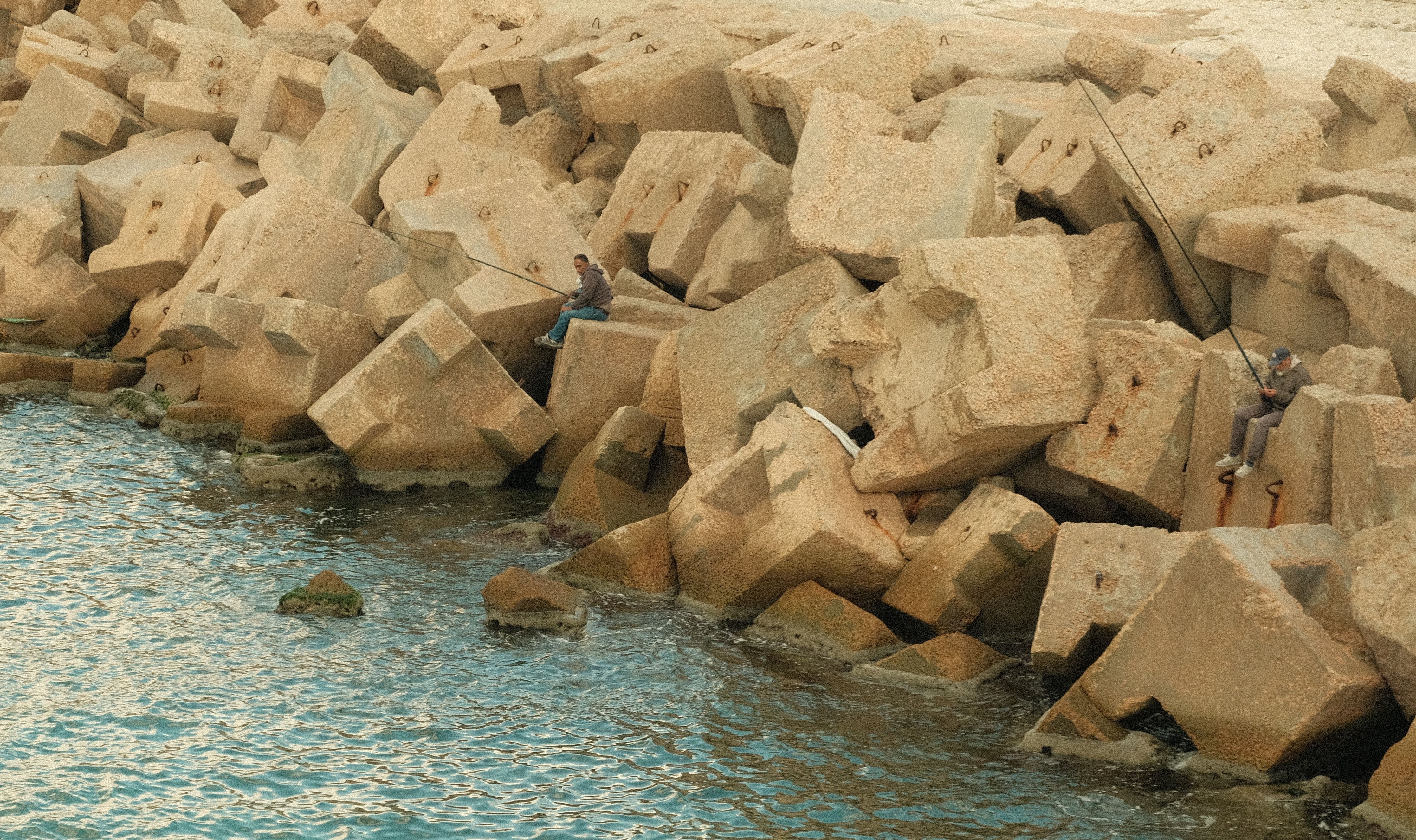 Fishermen Relaxing on Coastal Concrete Blocks · Free Stock Photo