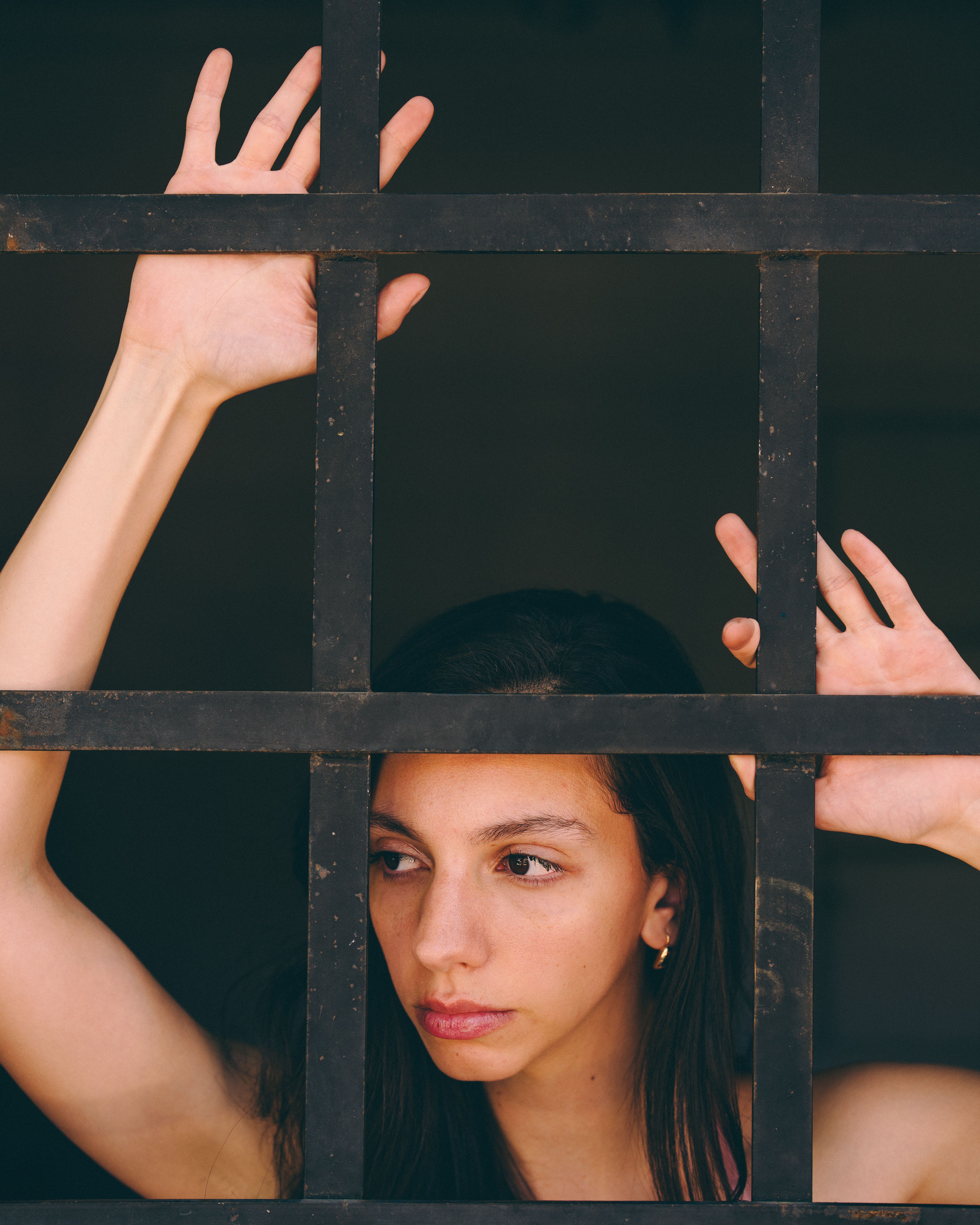 Woman Behind Bars with Reflective Expression · Free Stock Photo