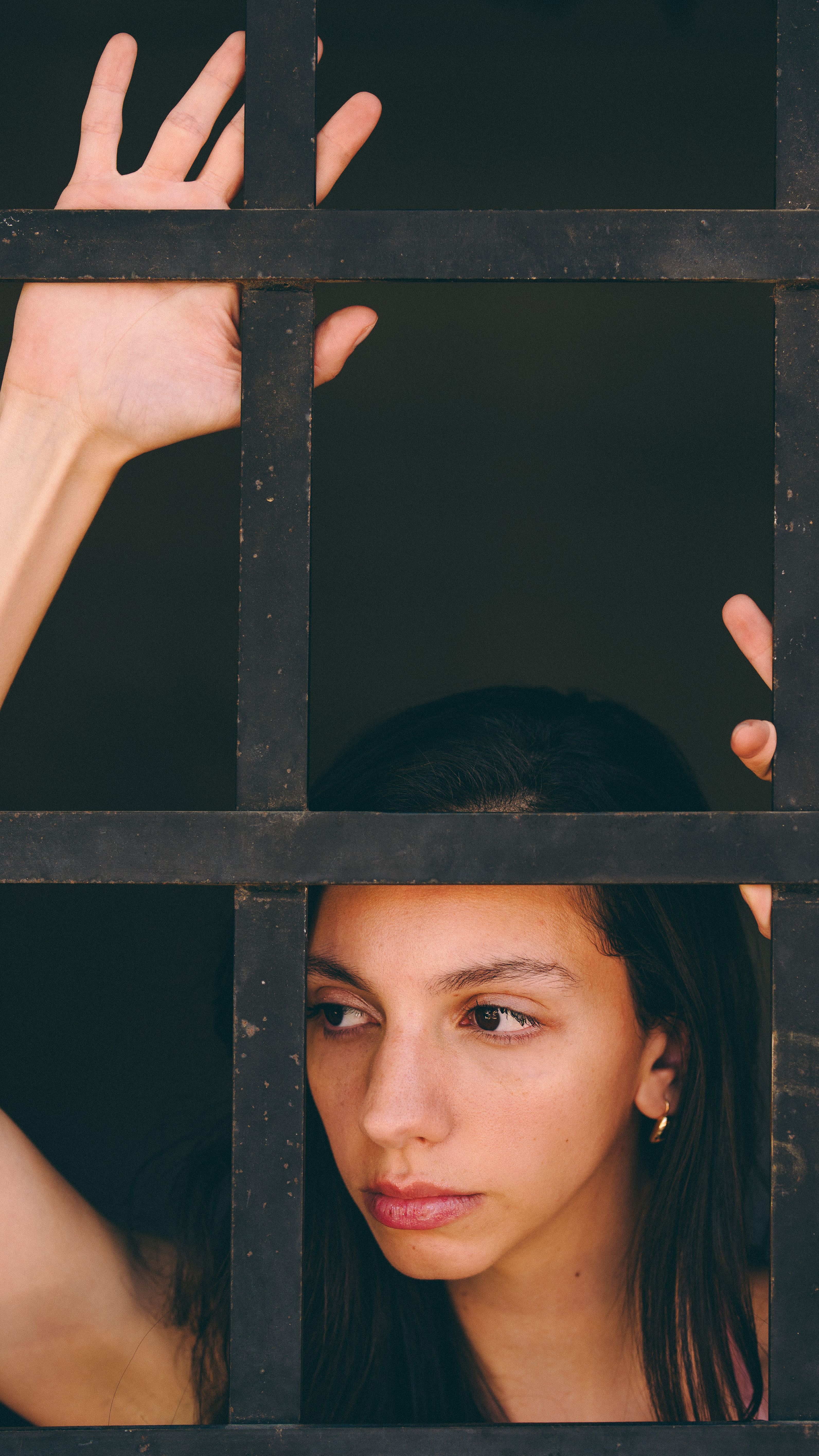 Contemplative Woman Gazing Through Bars · Free Stock Photo