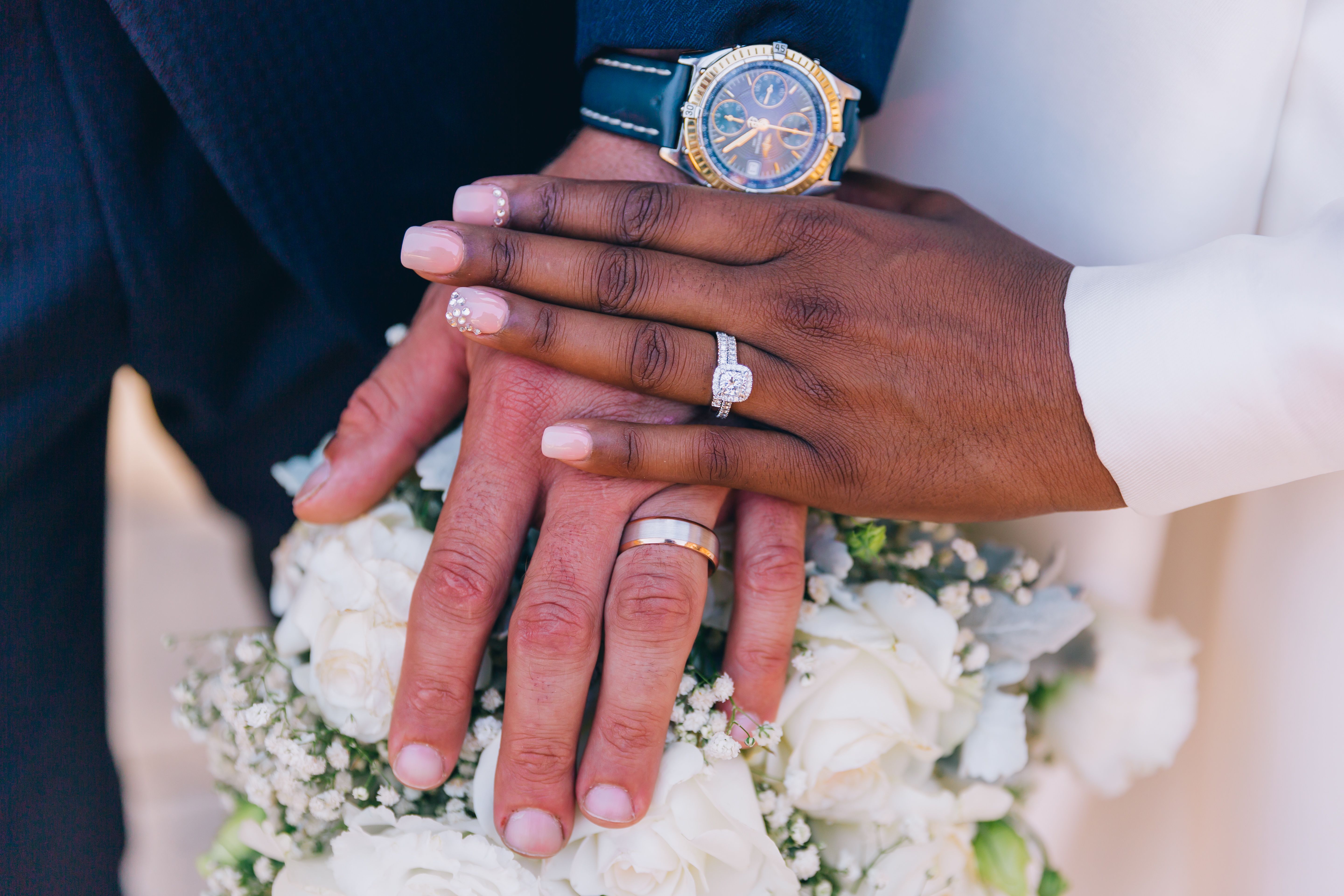 Elegant Wedding Rings on Couple's Hands Over Bouquet · Free Stock Photo