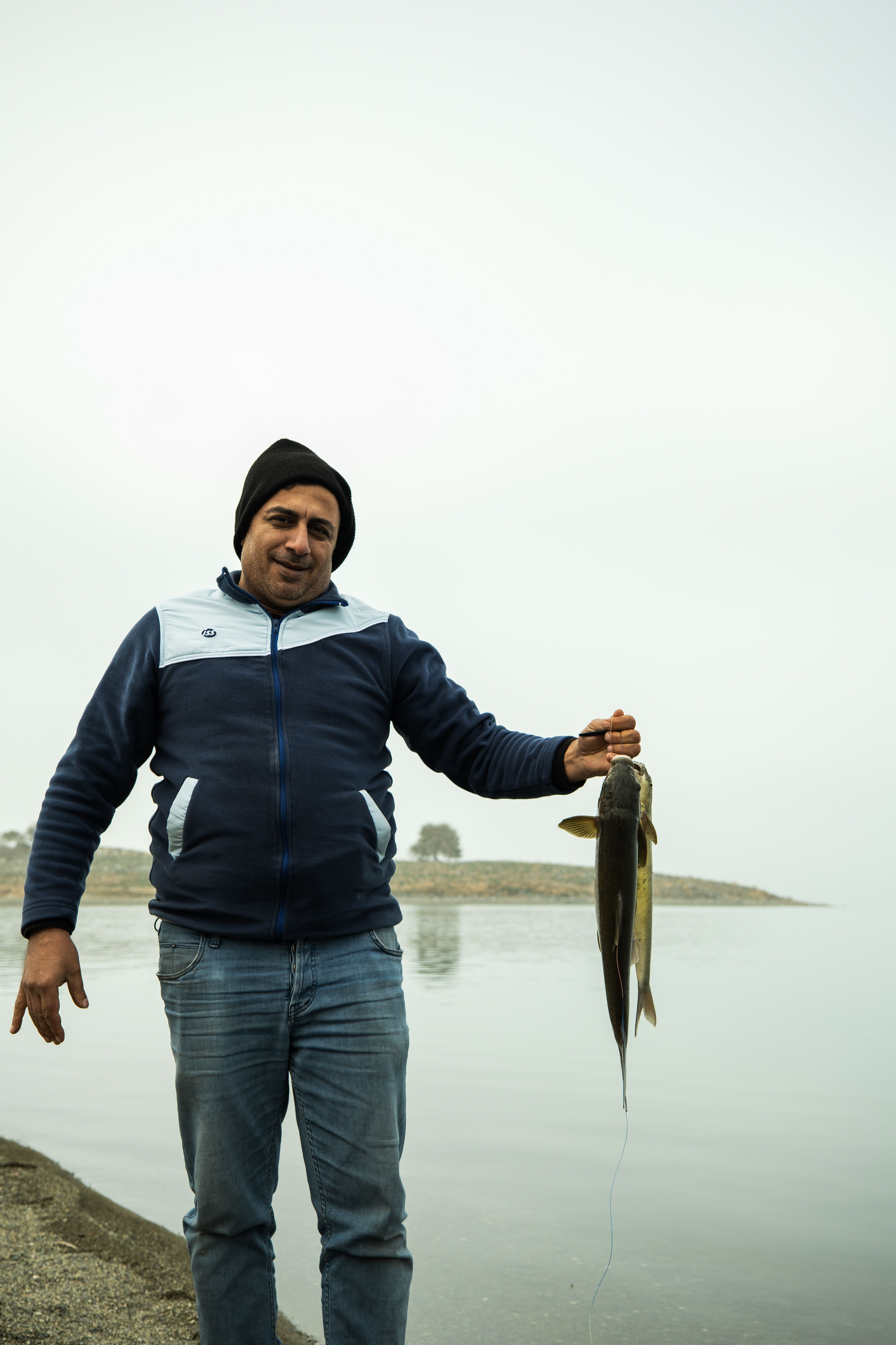 Man proudly holding freshly caught fish by lakeside · Free Stock Photo