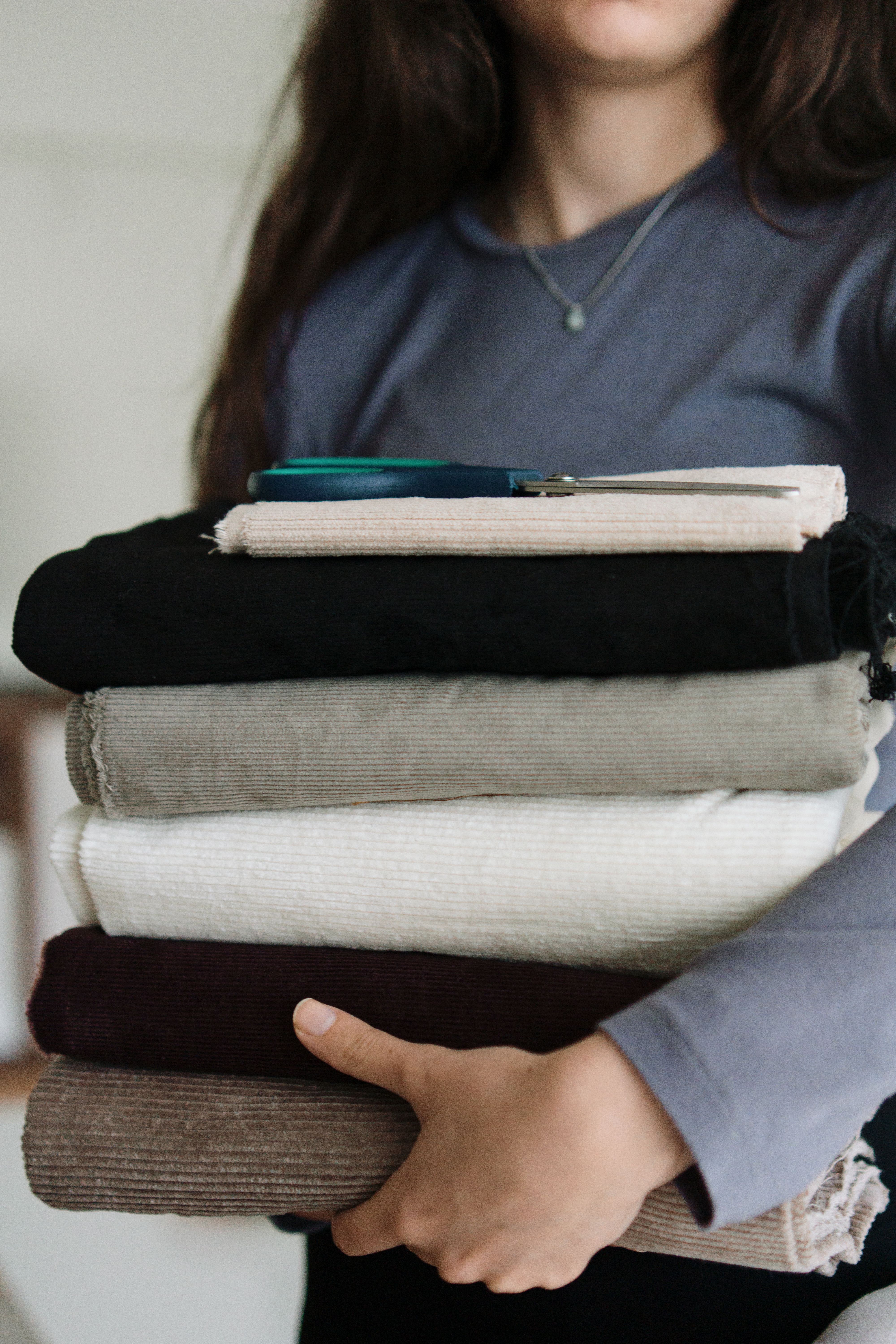 Person Holding a Stack of Folded Fabrics Indoors · Free Stock Photo