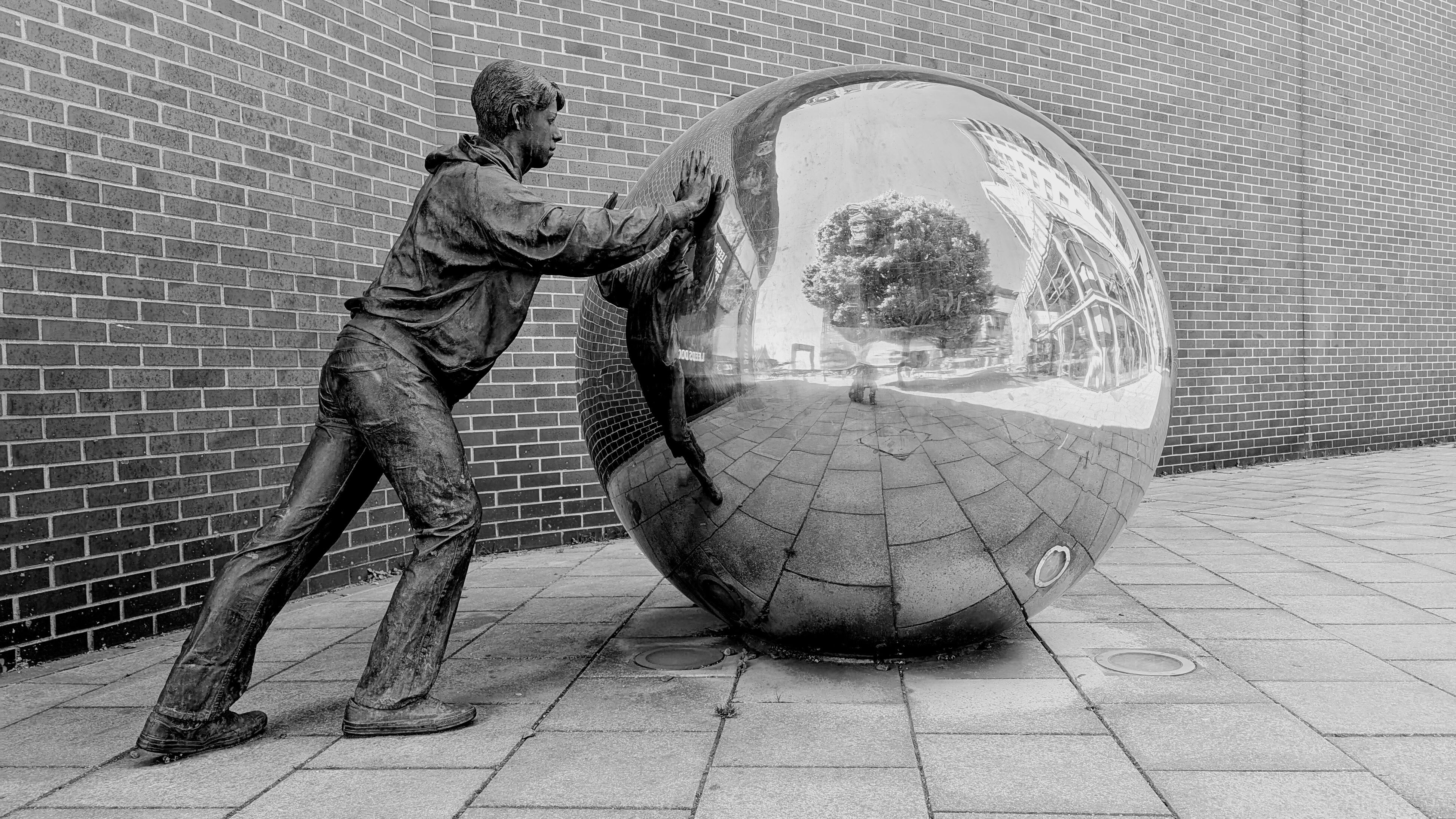 Monochrome Sculpture of Man Pushing Reflective Sphere · Free Stock Photo