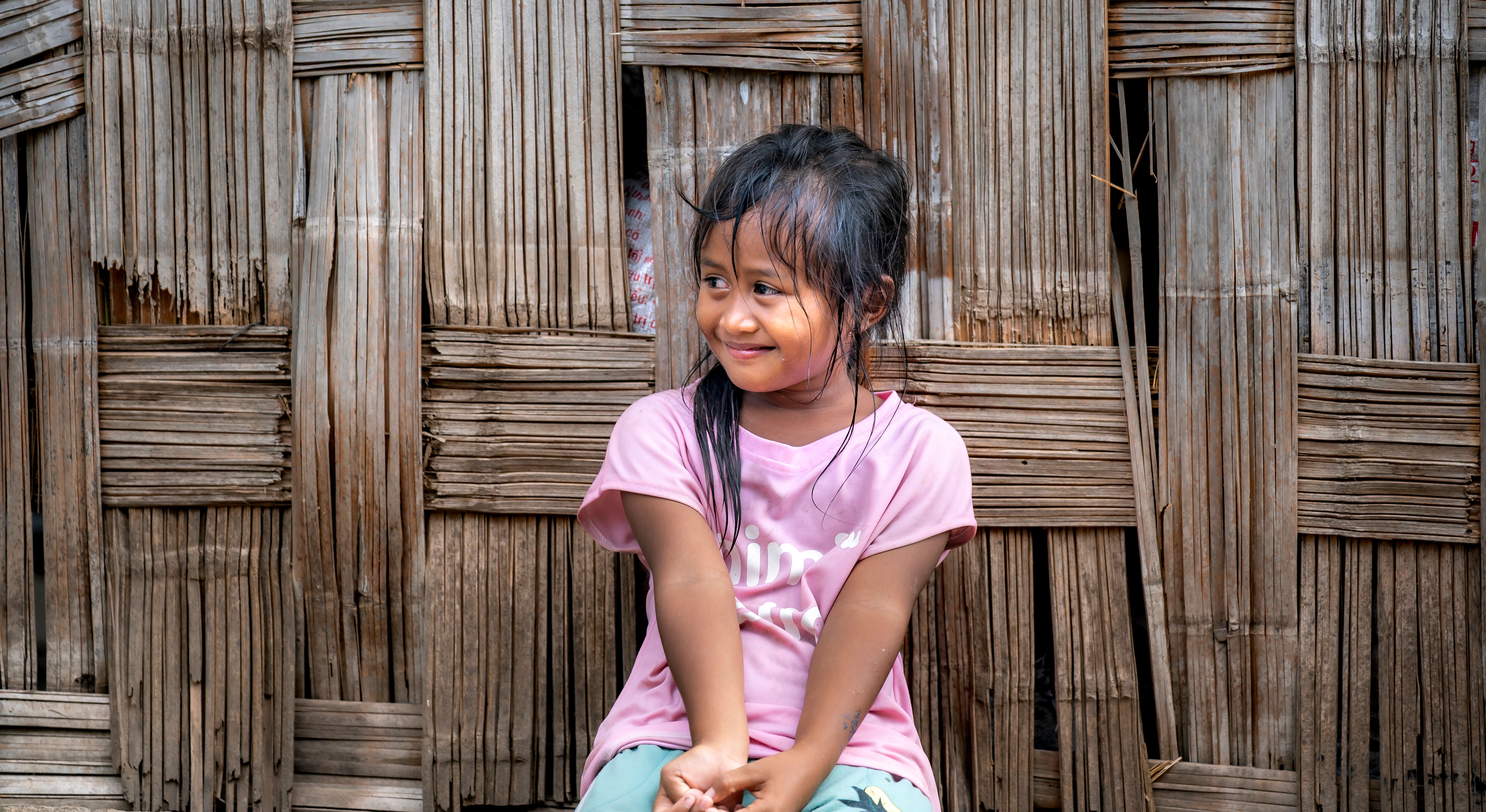 Happy Child Sitting by Woven Straw Wall · Free Stock Photo