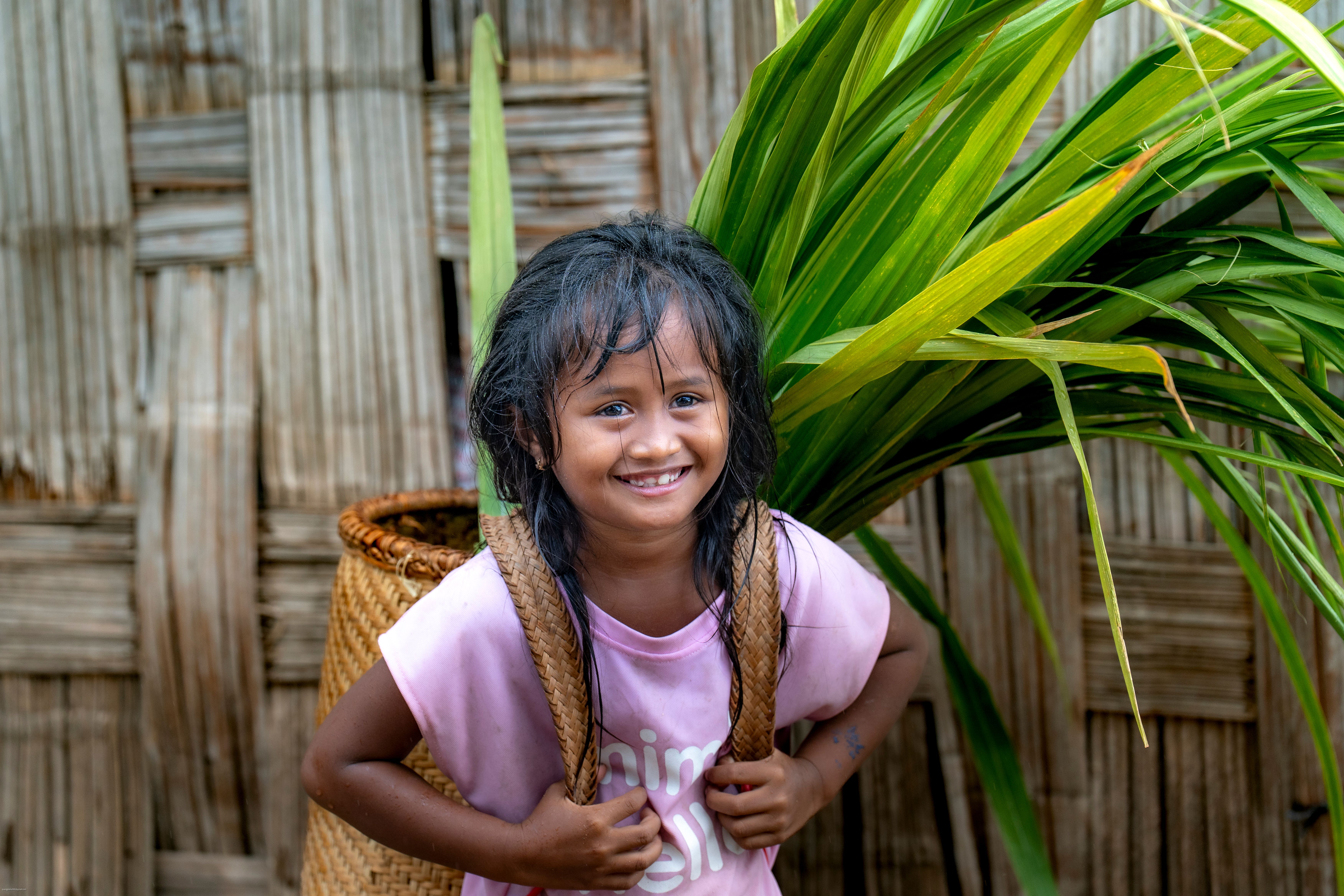Happy Child Sitting by Woven Straw Wall · Free Stock Photo