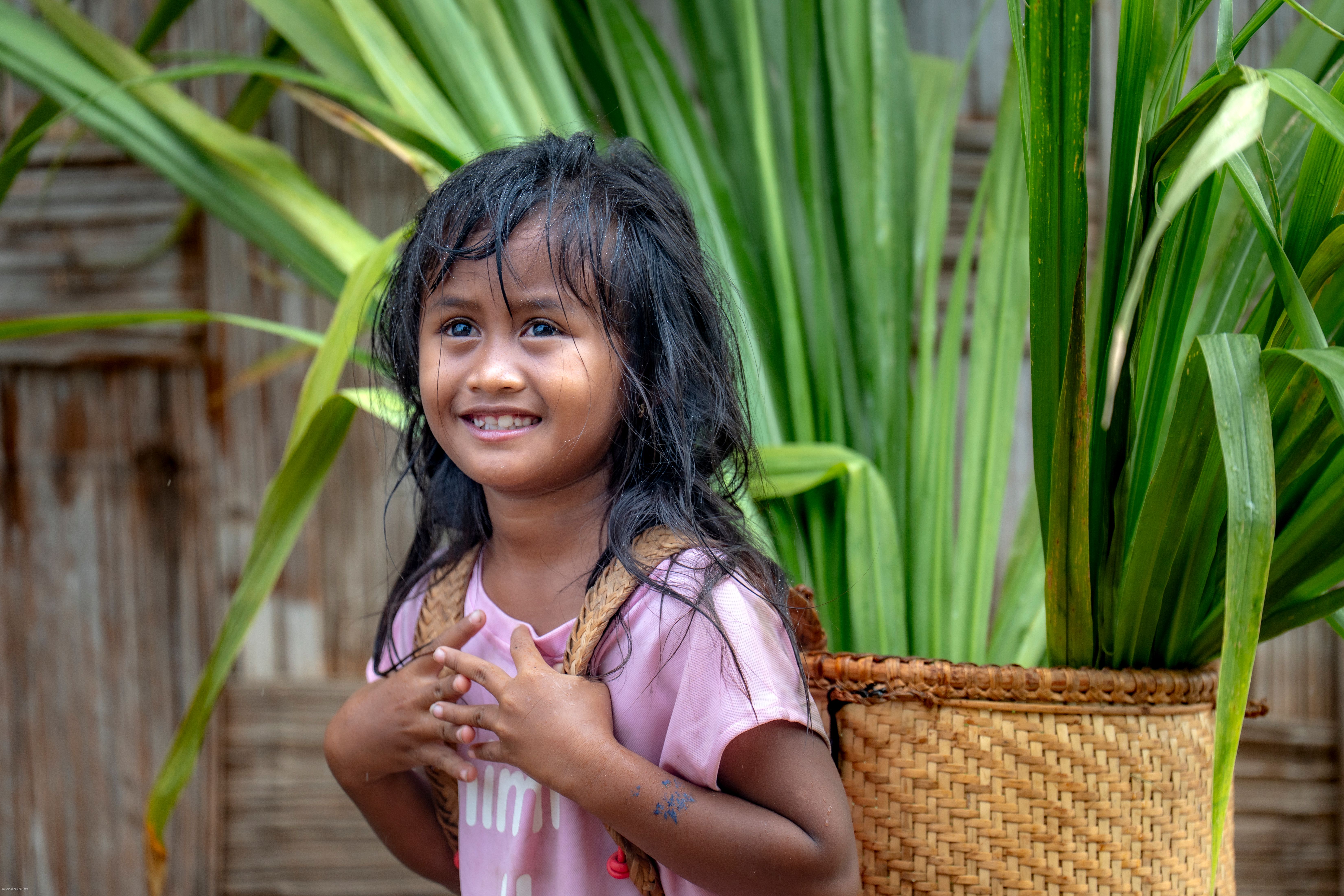 Happy Child Sitting by Woven Straw Wall · Free Stock Photo