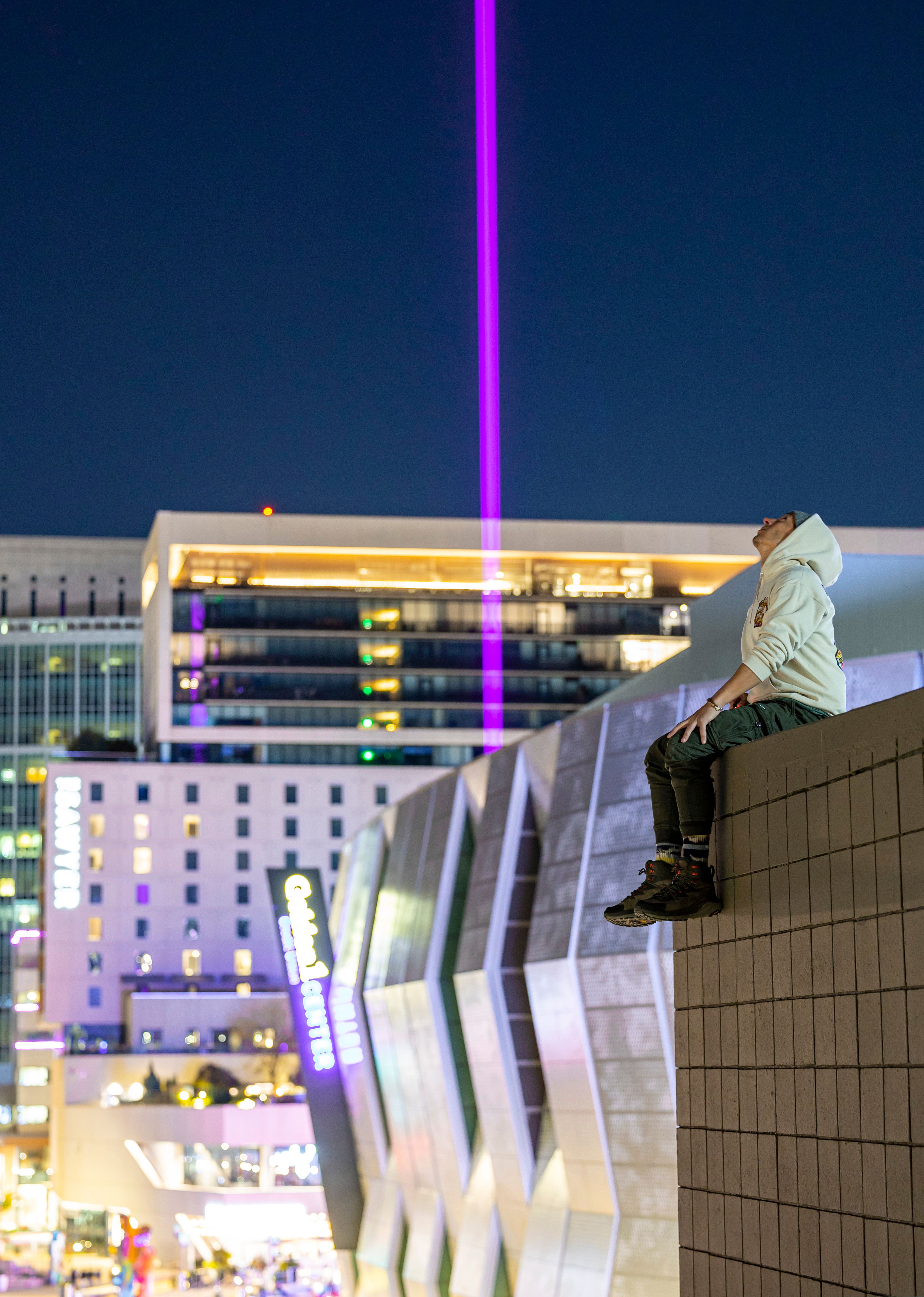 Person atop urban building with purple beam · Free Stock Photo