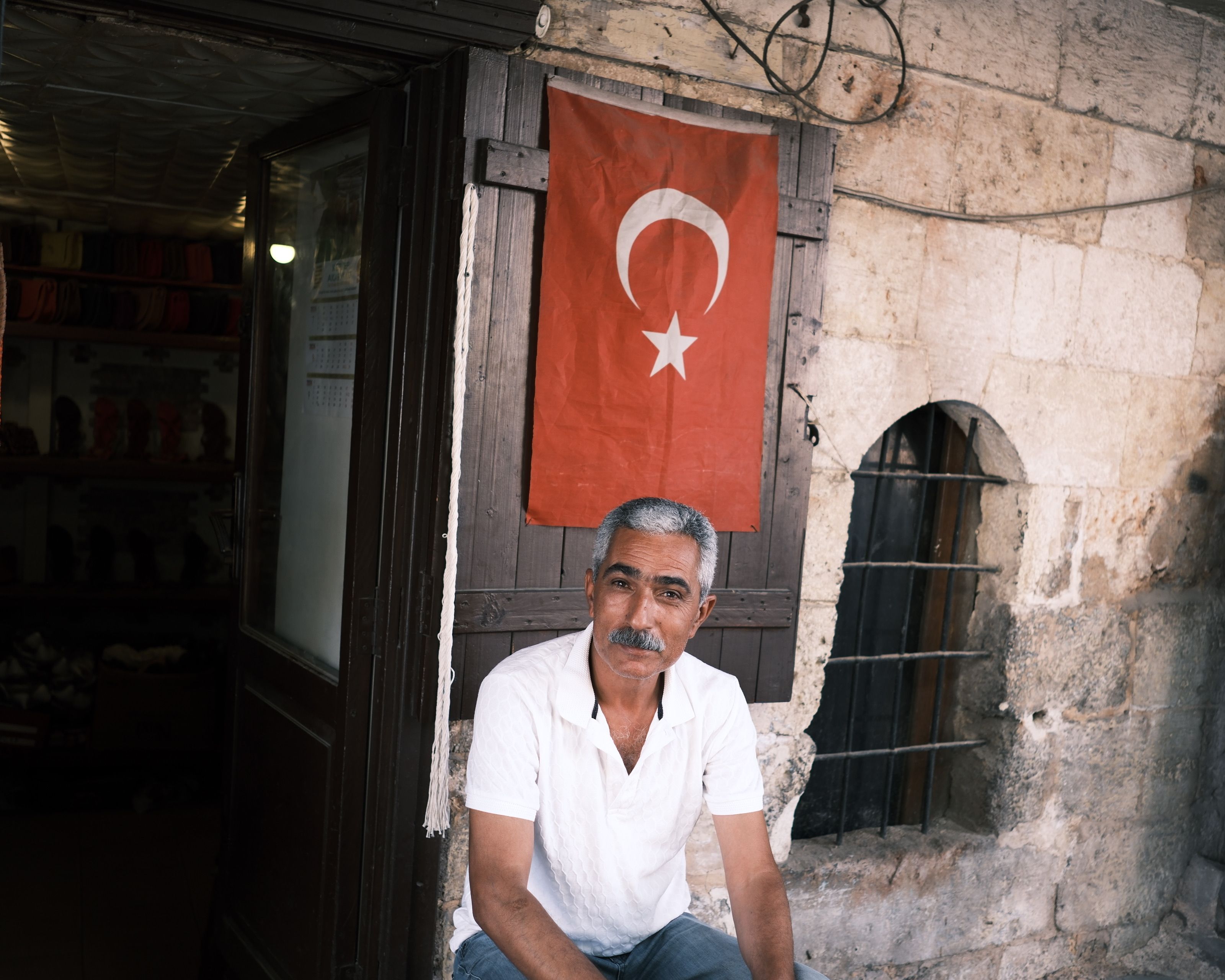 Portrait of man sitting outside shop with Turkish flag · Free Stock Photo