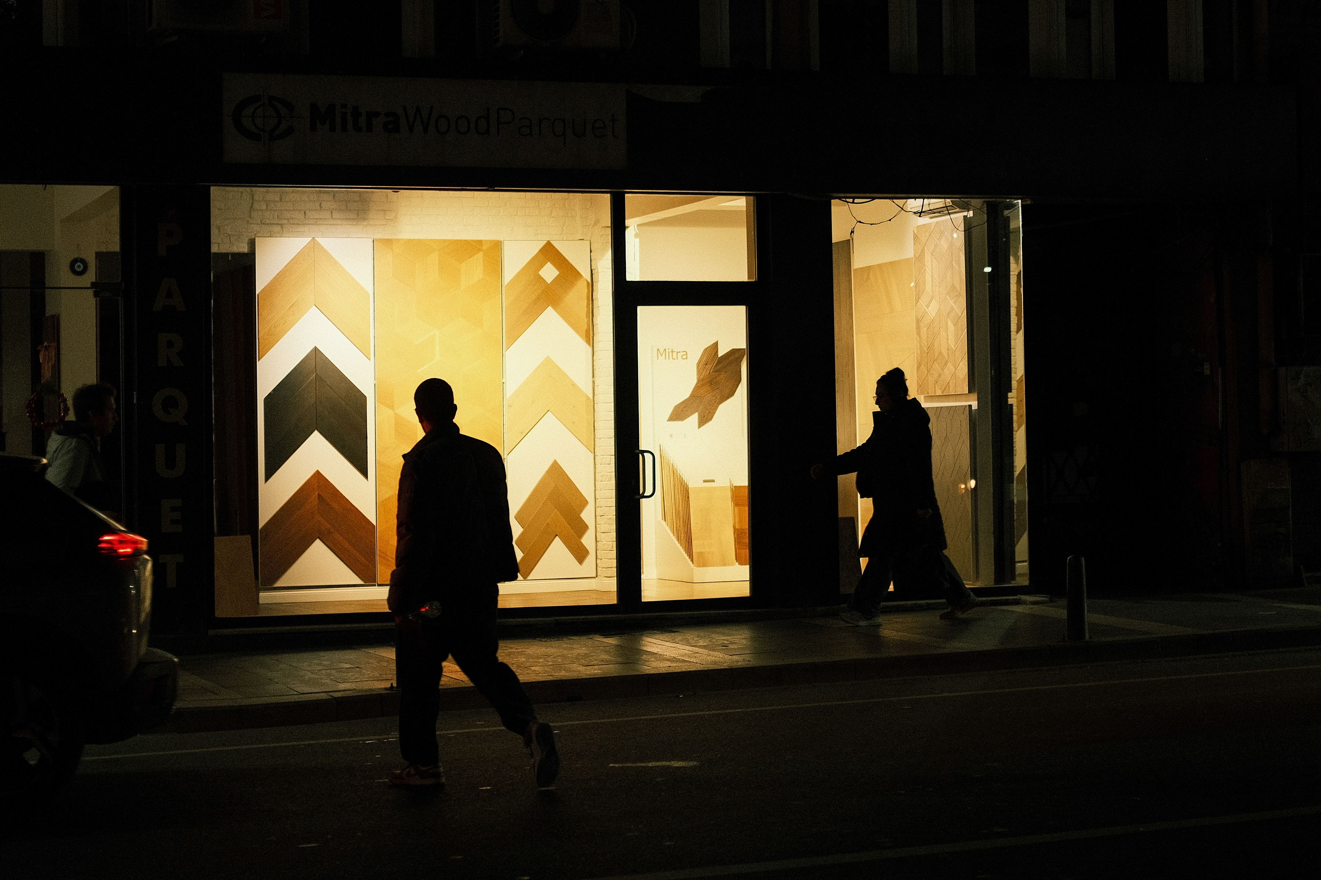 Silhouetted Figures Passing a Parquet Store at Night · Free Stock Photo