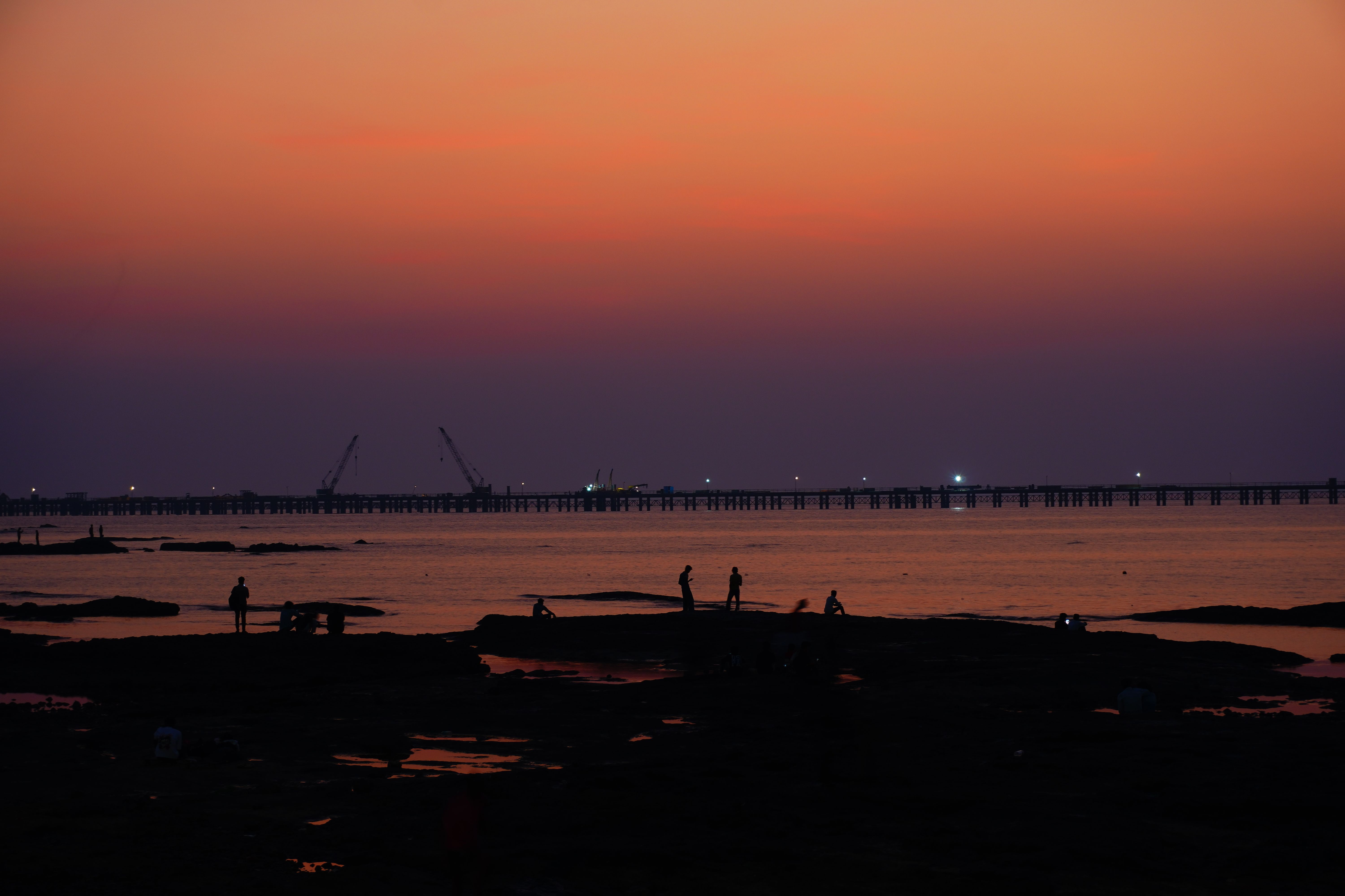 Silhouetted Figures at a Coastal Sunset · Free Stock Photo