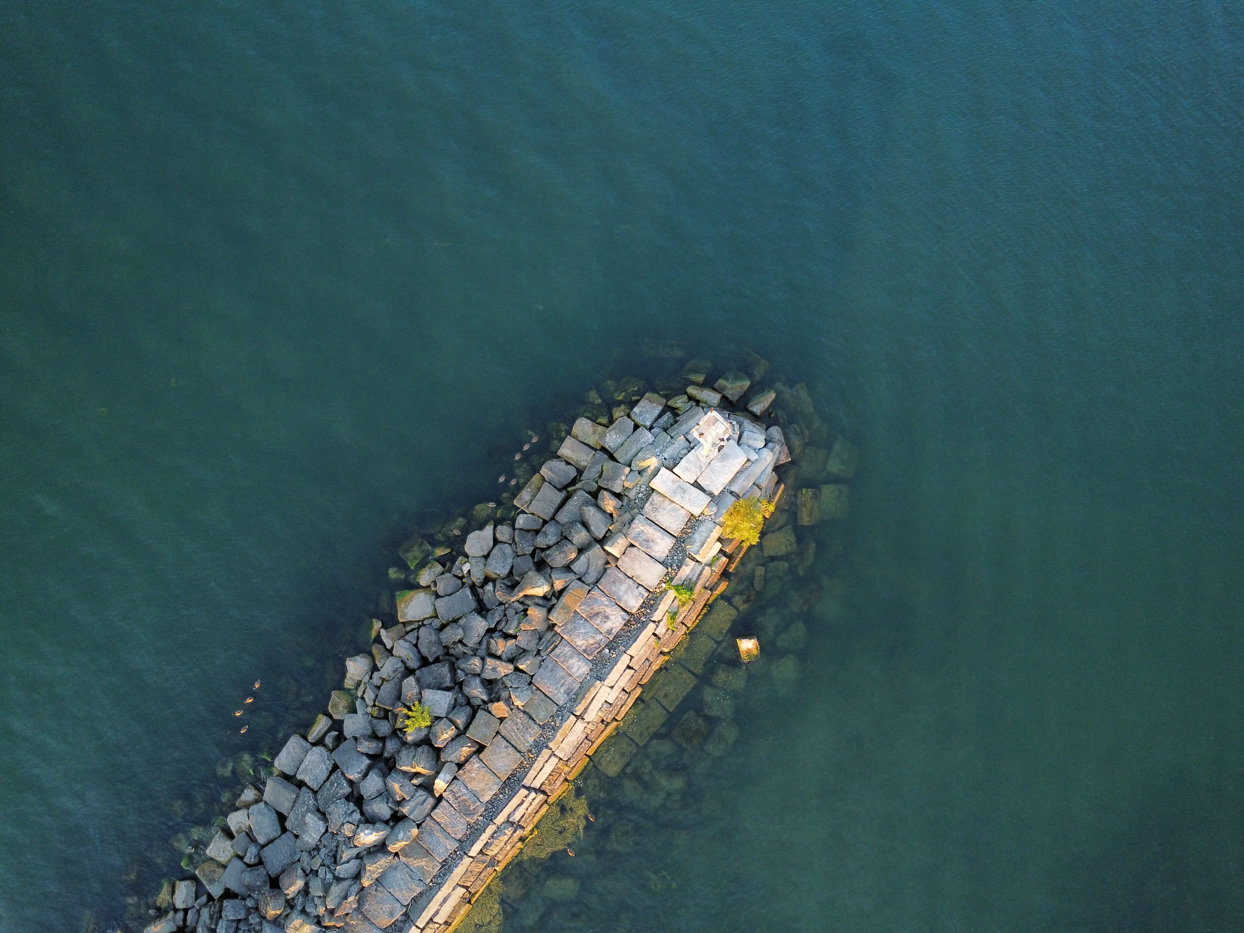 Aerial View of Rocky Pier Extending into Blue Water · Free Stock Photo