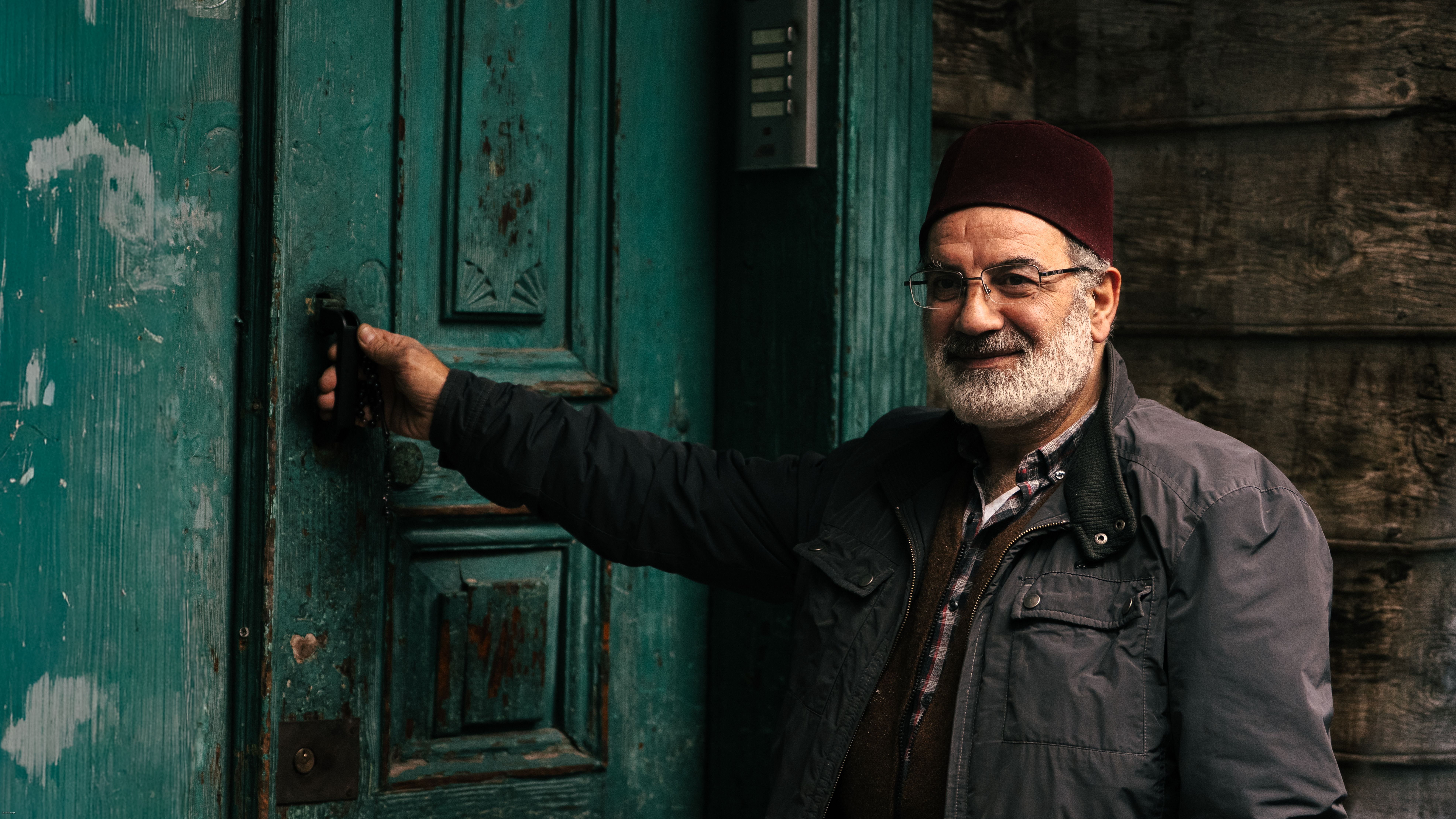 Elderly man in traditional attire at rustic wooden door · Free Stock Photo