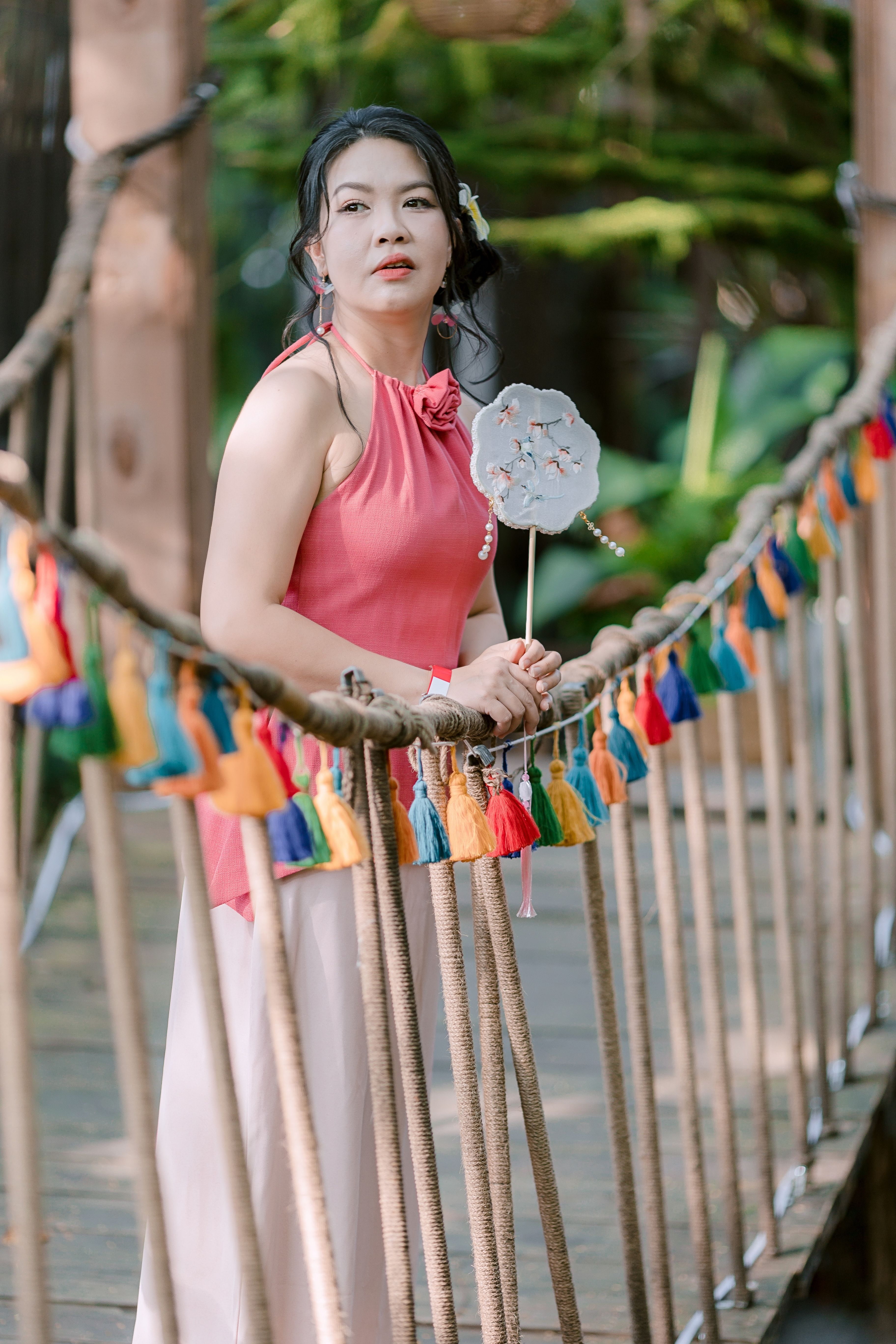 Young Woman Holding Fan on Vibrant Roped Bridge · Free Stock Photo