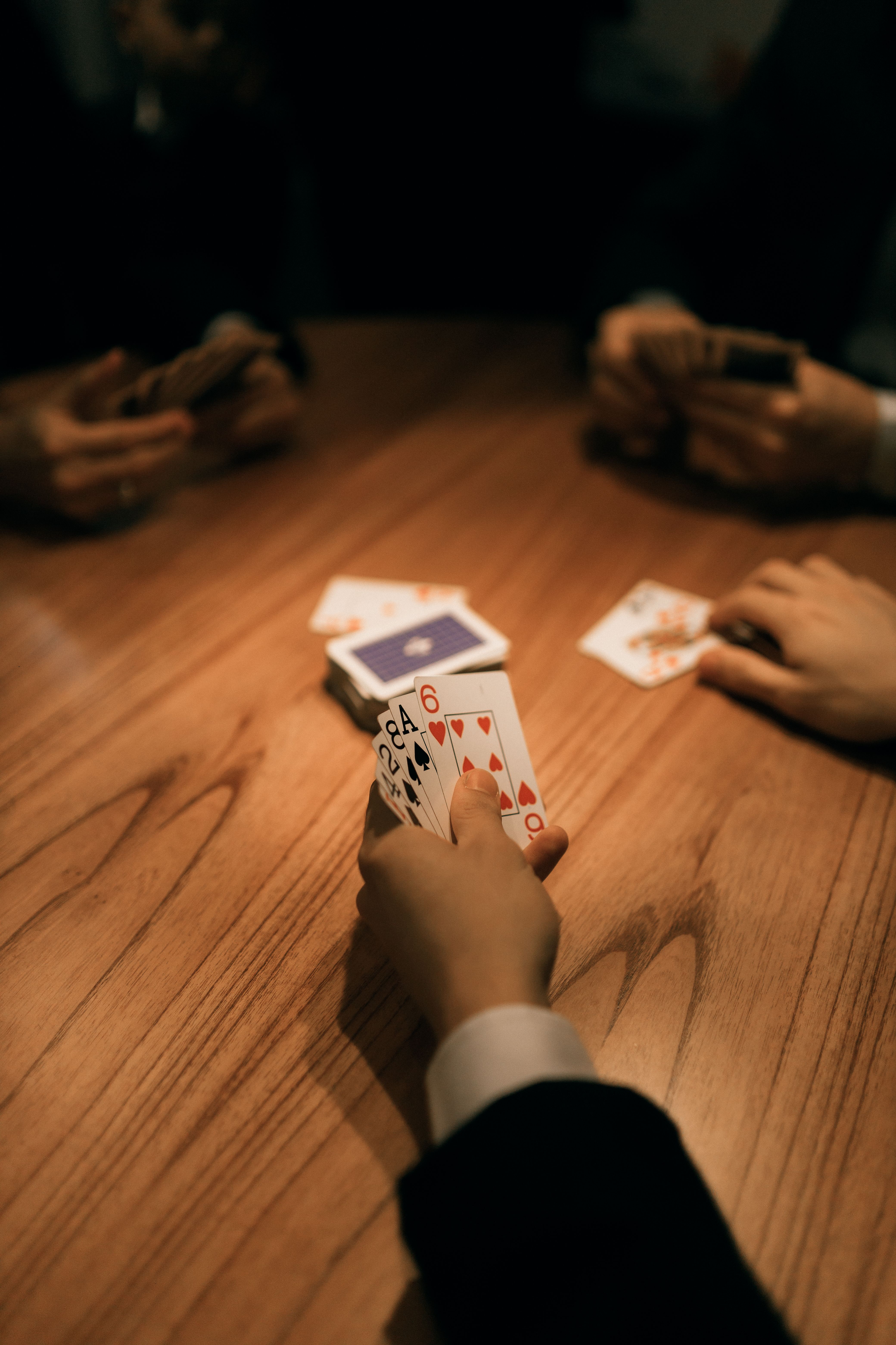 Group Playing Cards at Wooden Table in Dim Light · Free Stock Photo
