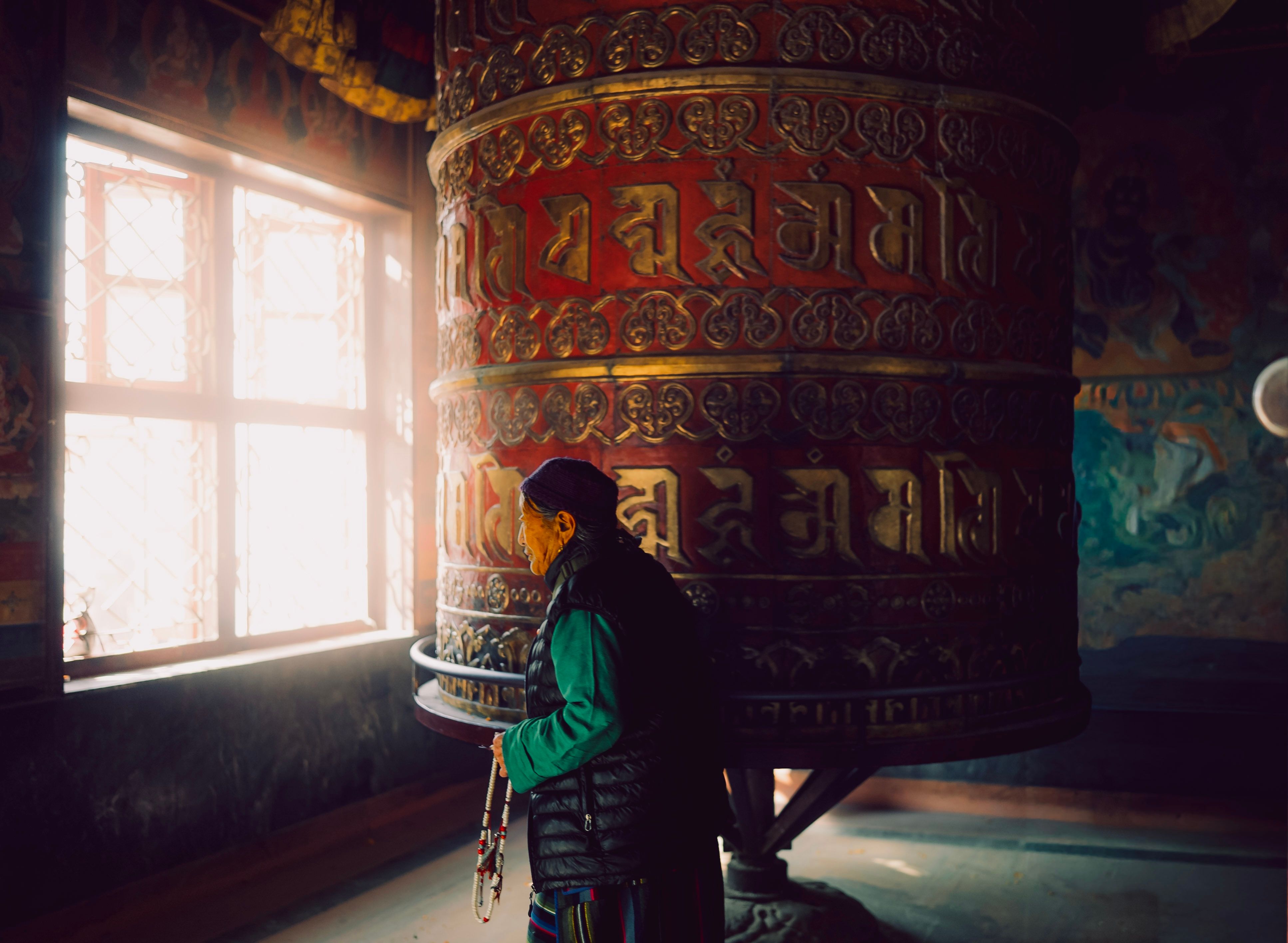 Elderly Woman by Tibetan Prayer Wheel in Monastery · Free Stock Photo