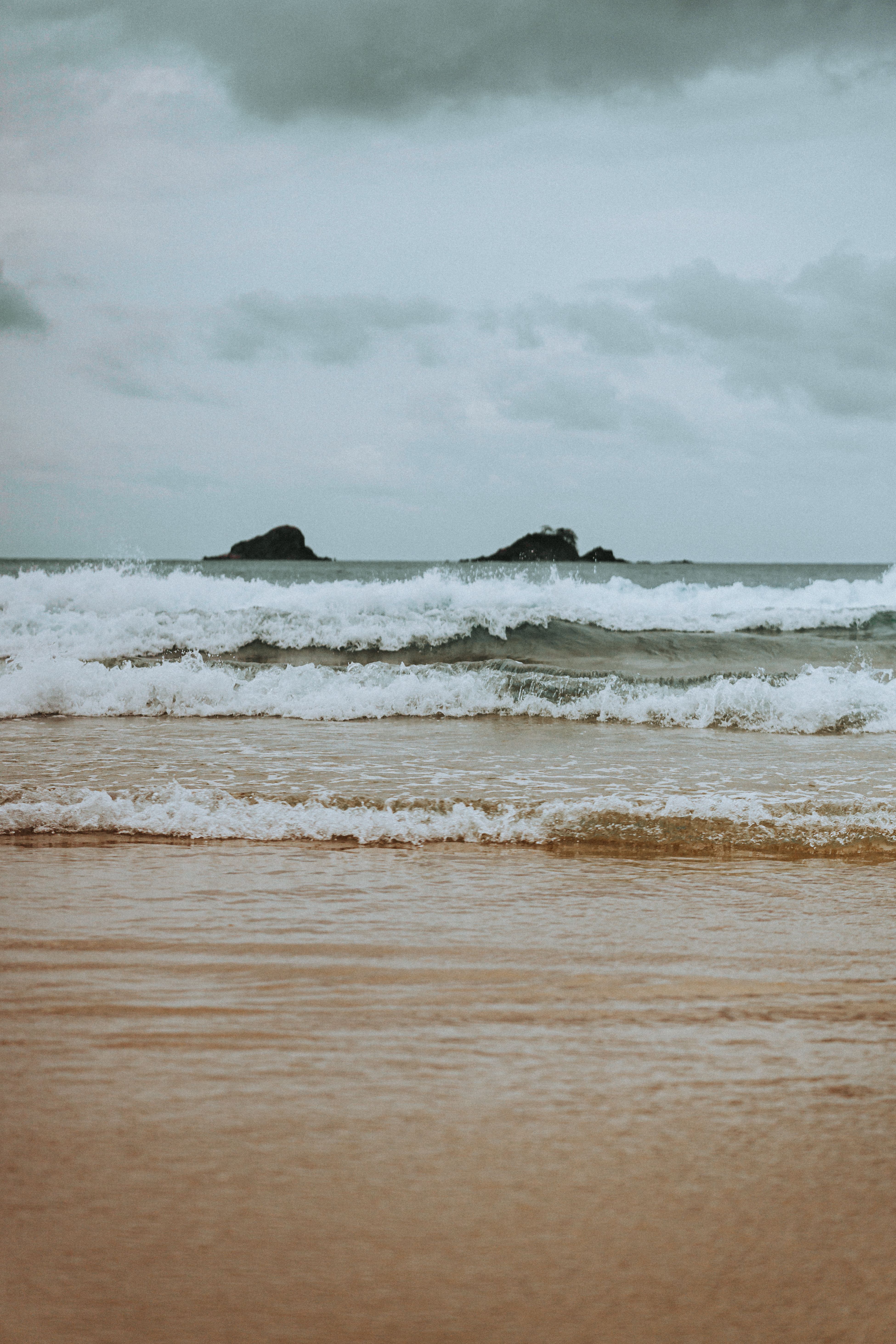 Waves Crashing on Sandy Beach with Overcast Sky · Free Stock Photo