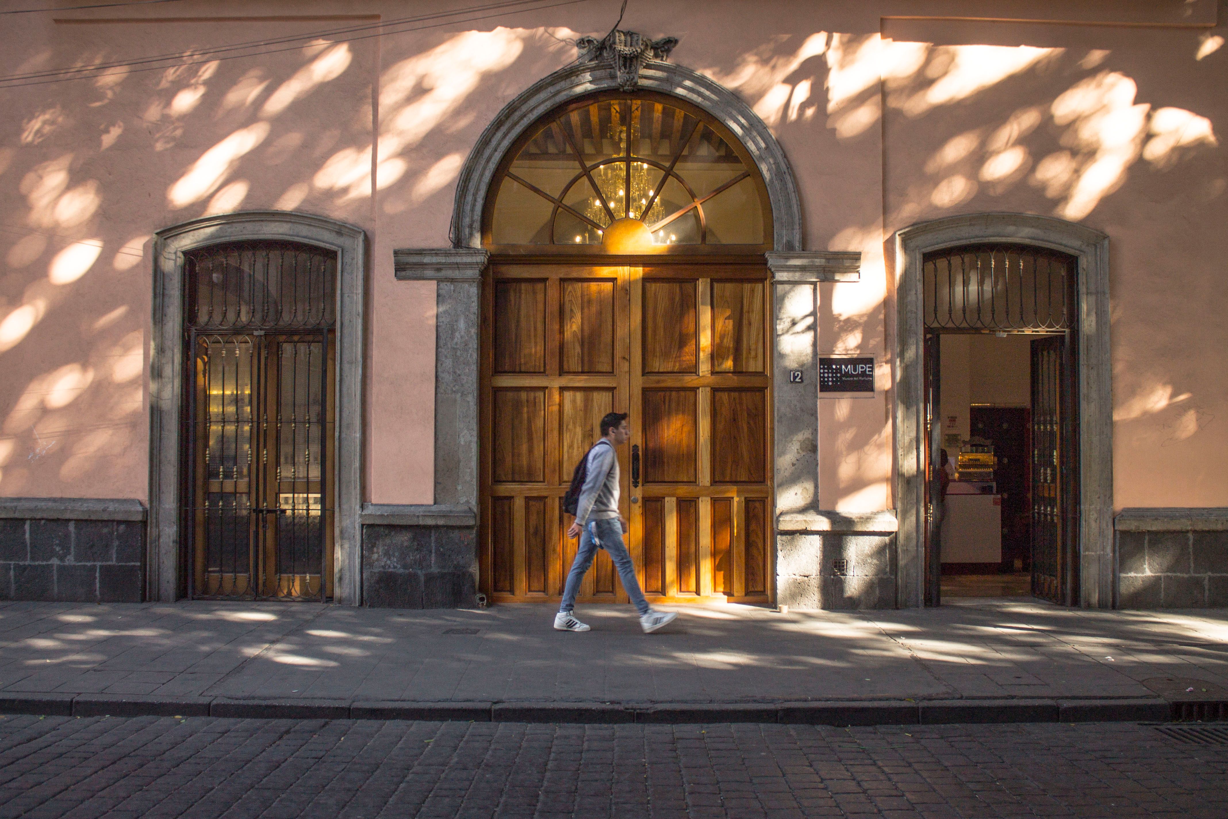 Young Man Walking Past Historic Building Entrance · Free Stock Photo