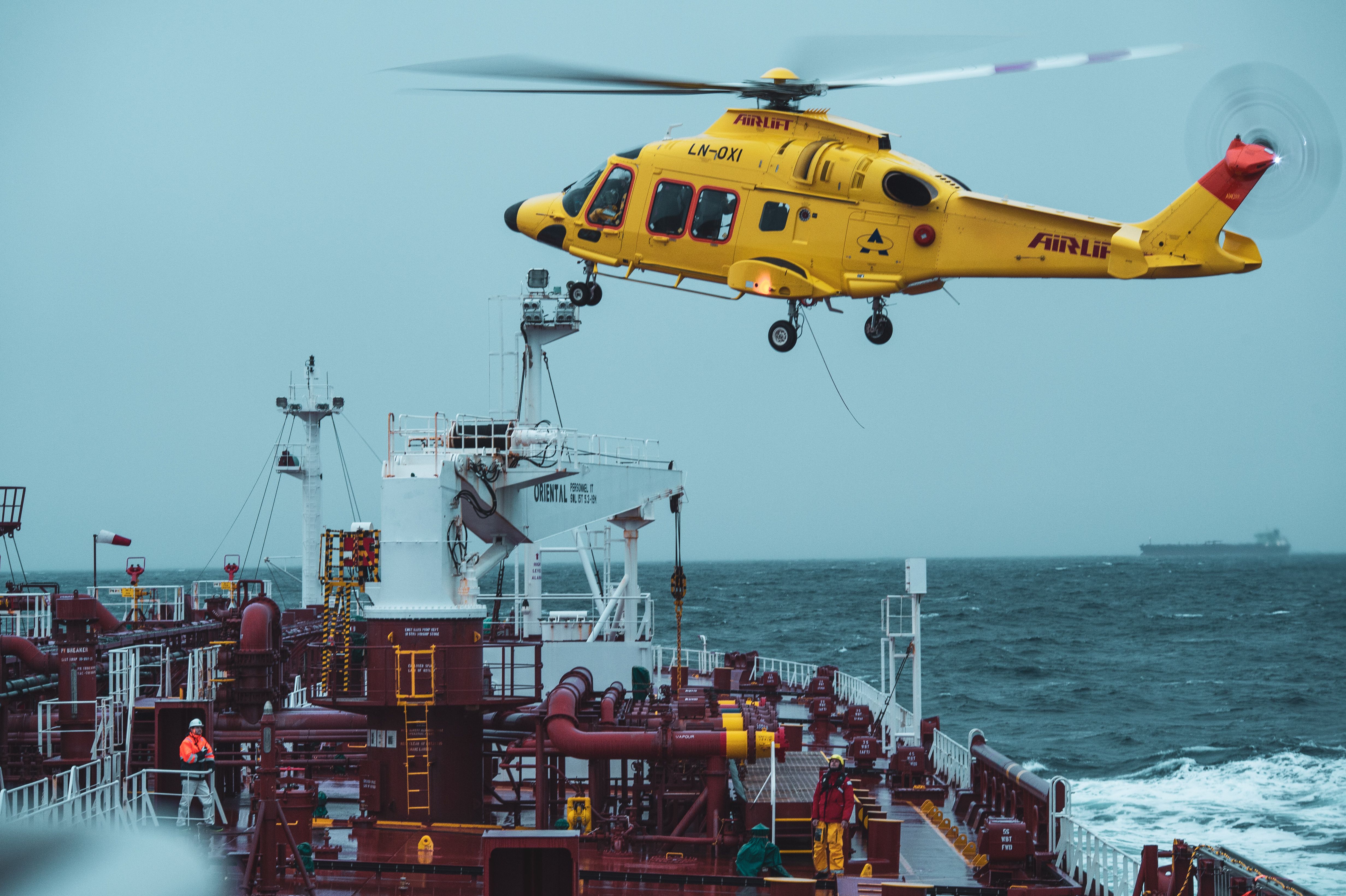Yellow Helicopter Hovering Above Cargo Ship at Sea · Free Stock Photo