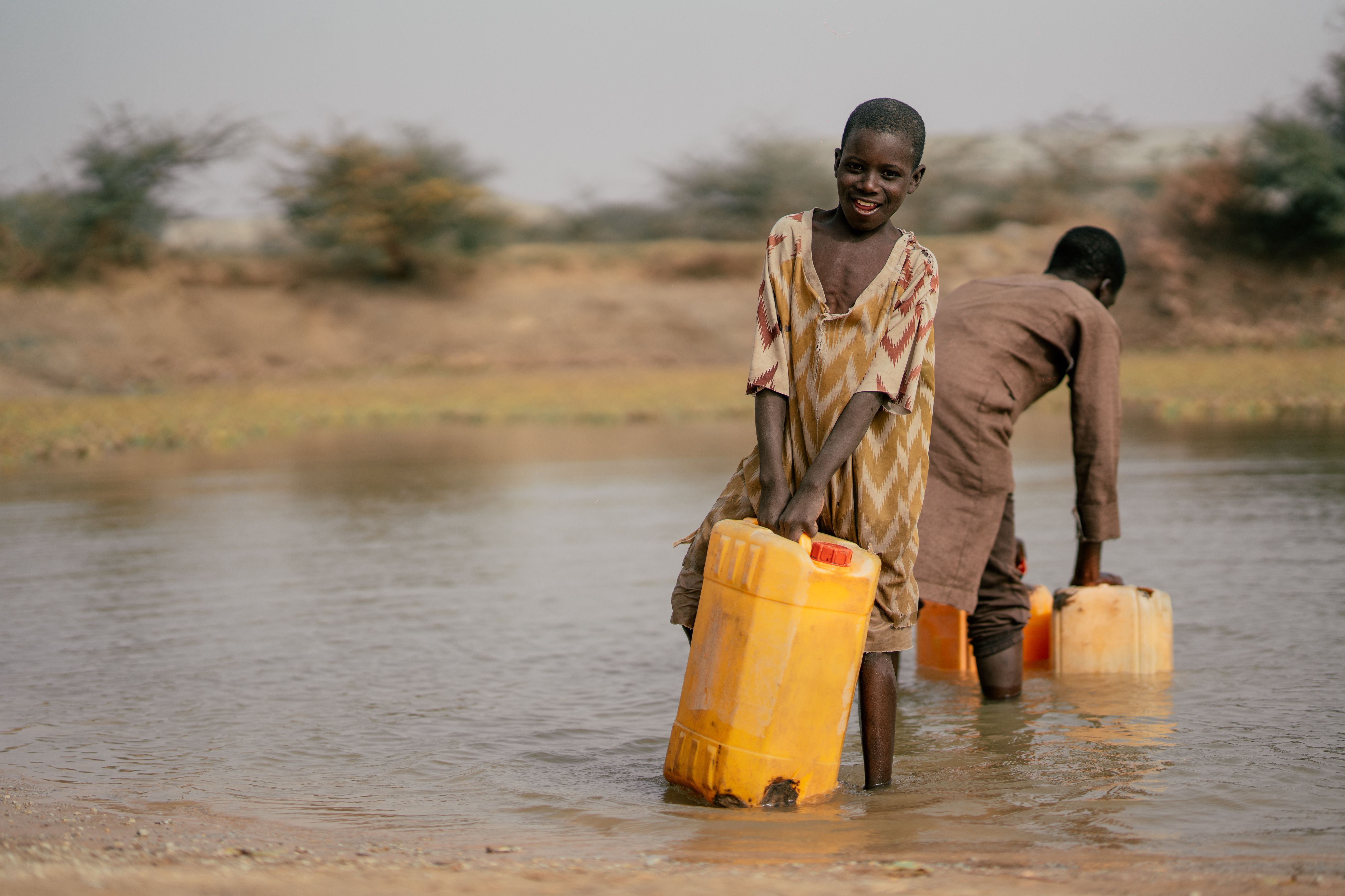 Children Carrying Water from a River Outdoors · Free Stock Photo