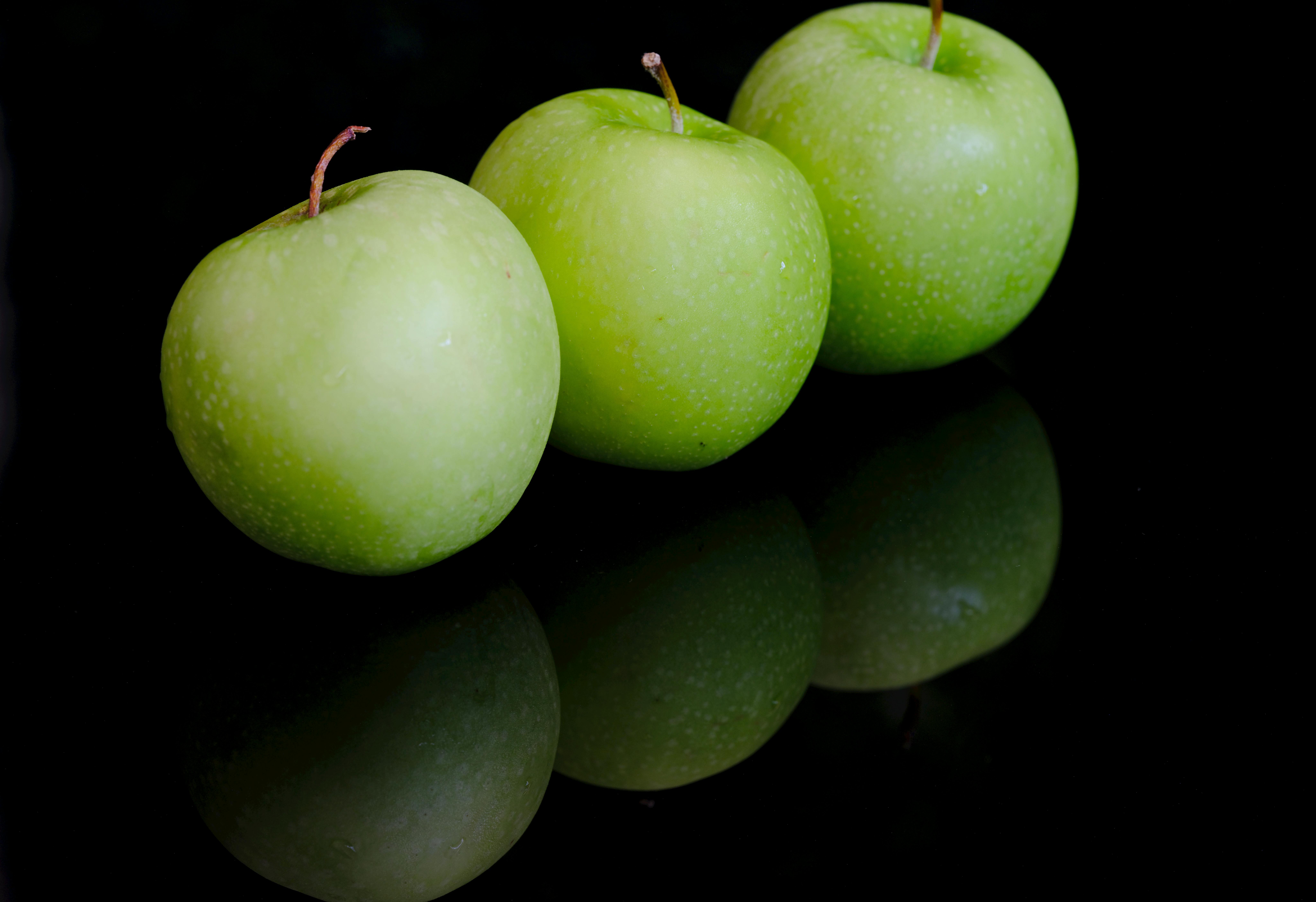 Three Fresh Green Apples on Black Reflective Background · Free Stock Photo