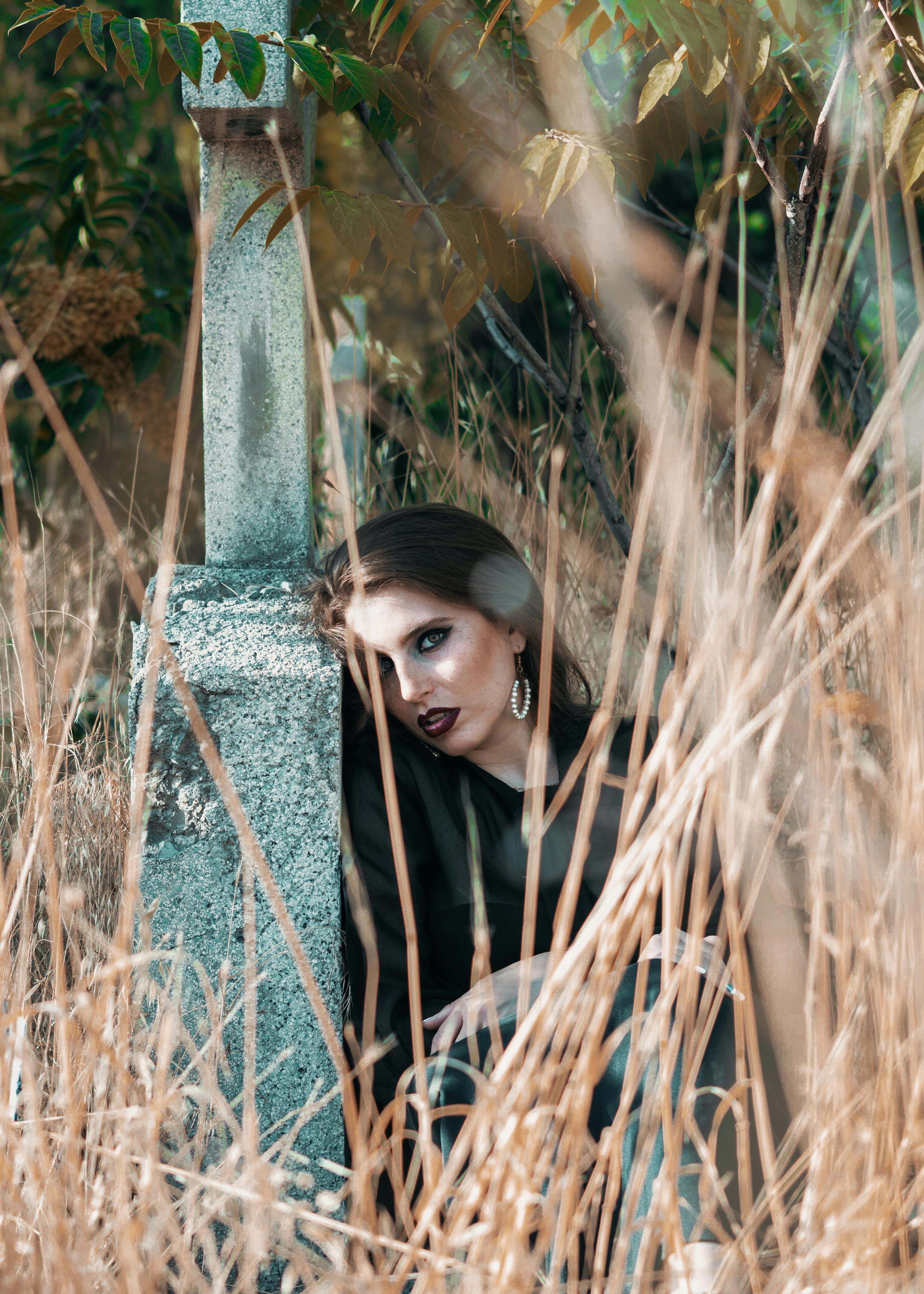 Young woman sitting on grave near cross in dried grass · Free Stock Photo