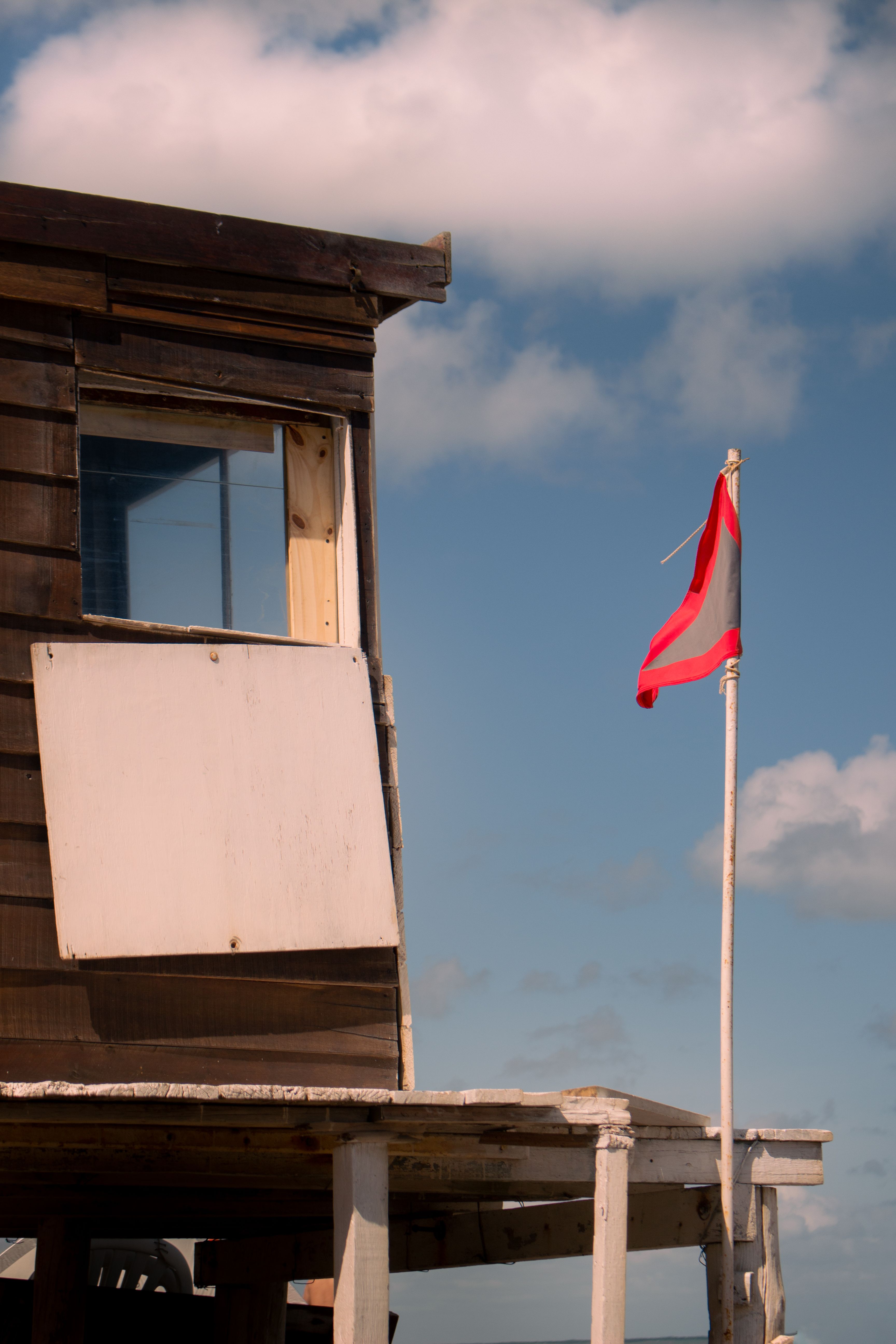 Rustic Lifeguard Hut with Red Flag Against Blue Sky · Free Stock Photo
