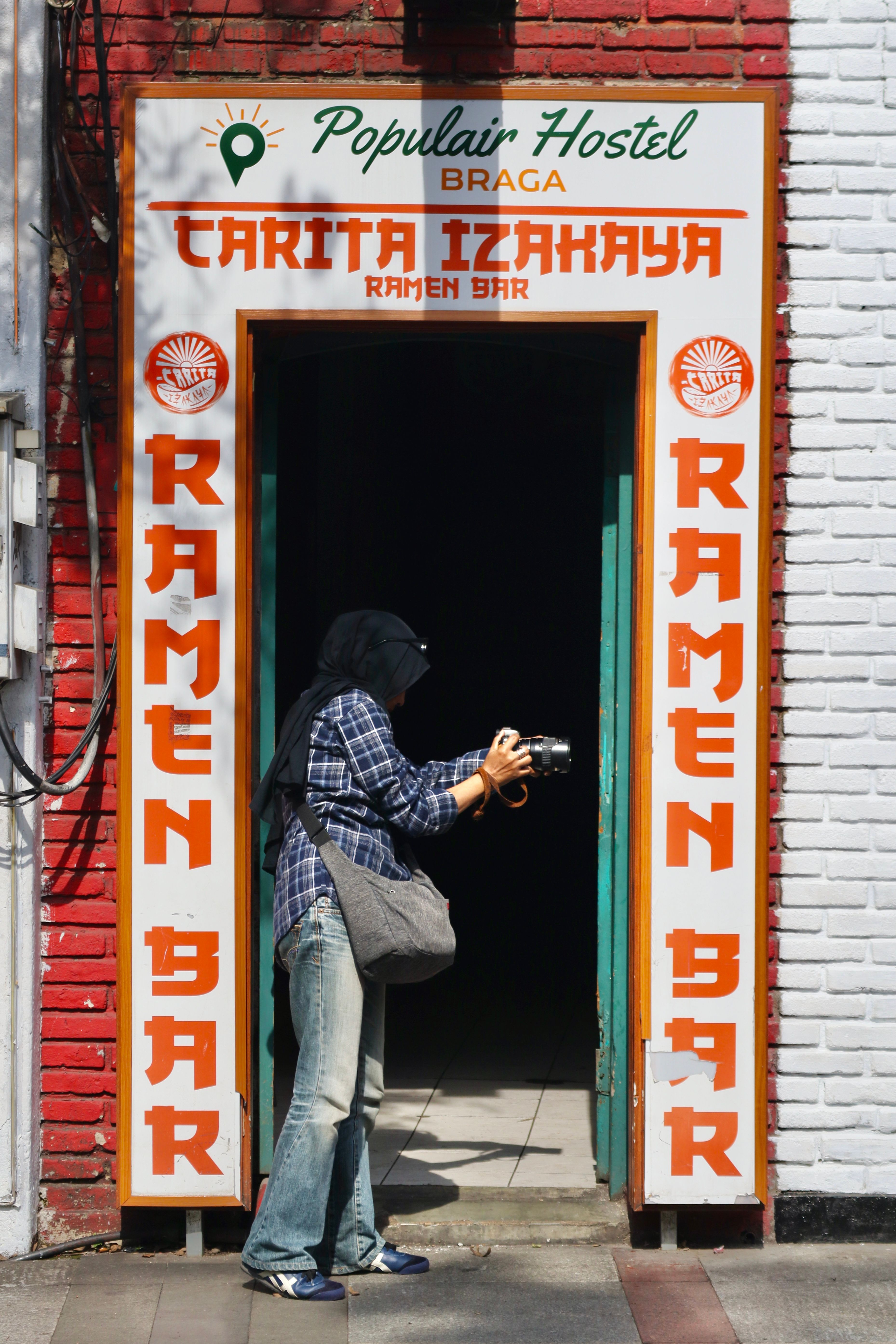 Woman entering a ramen bar with camera in hand · Free Stock Photo