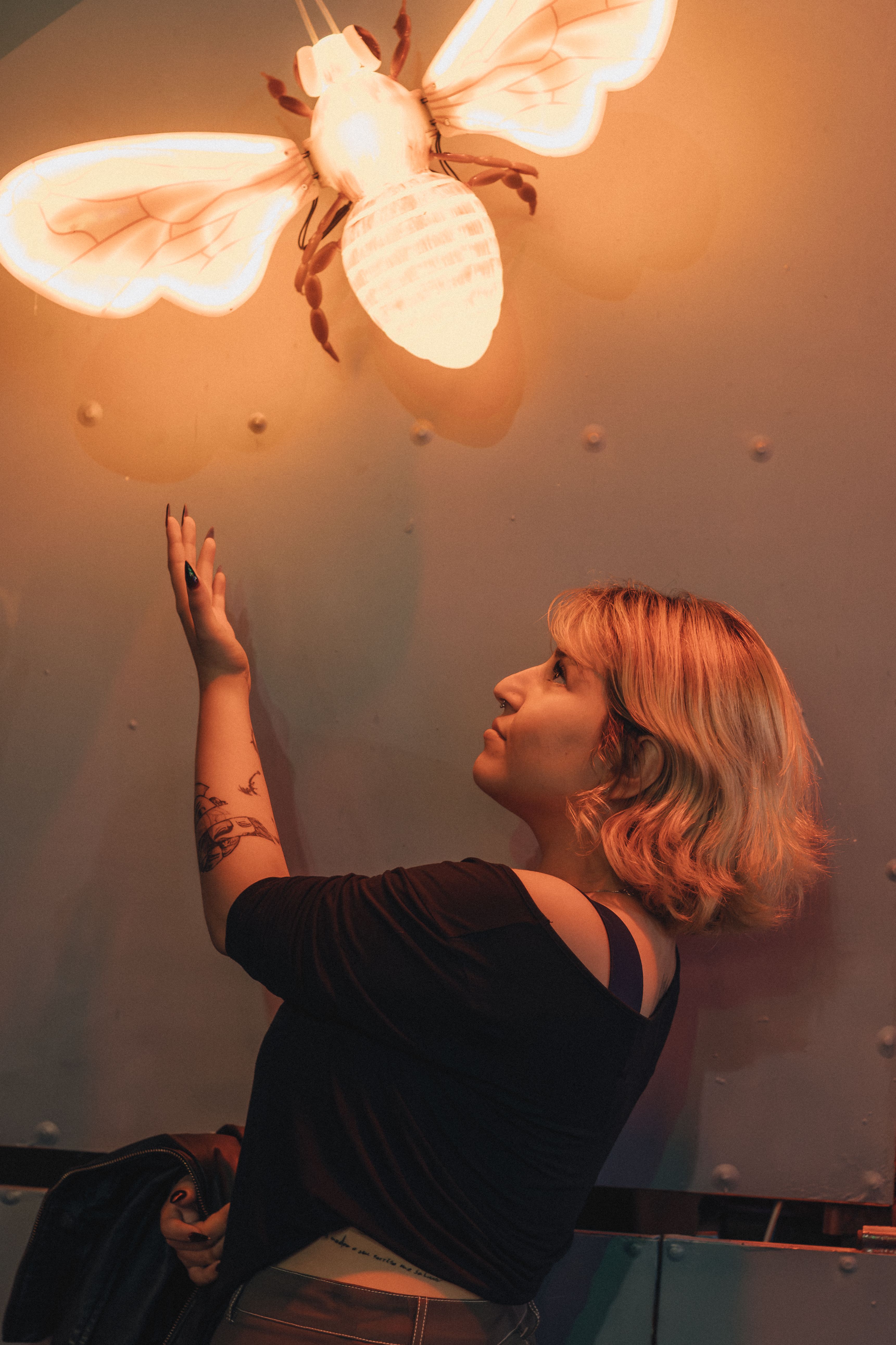 Woman Admiring Illuminated Bee Wall Art at Night · Free Stock Photo