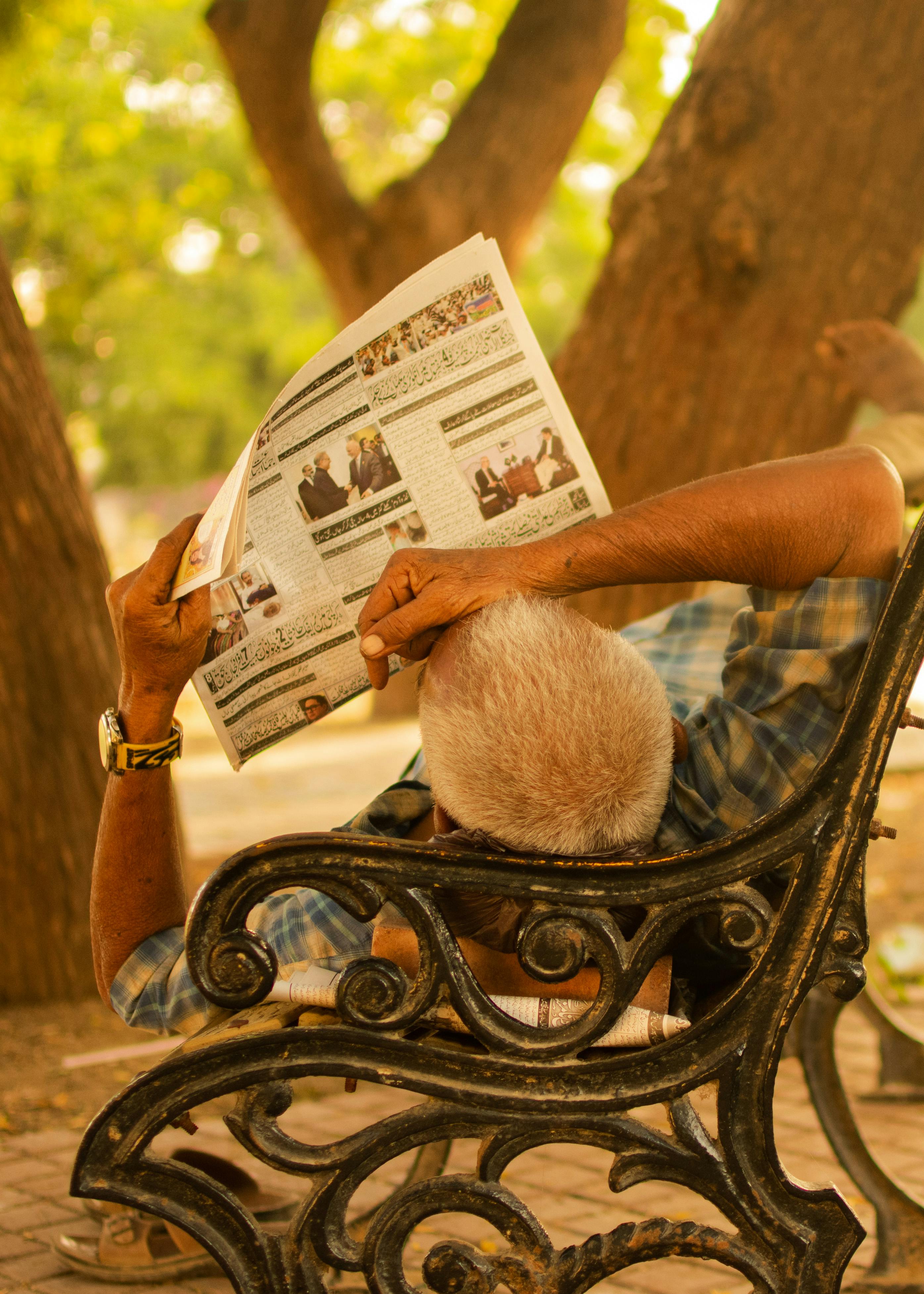 Person Reading Newspaper Lying on Black Metal Bench · Free Stock Photo