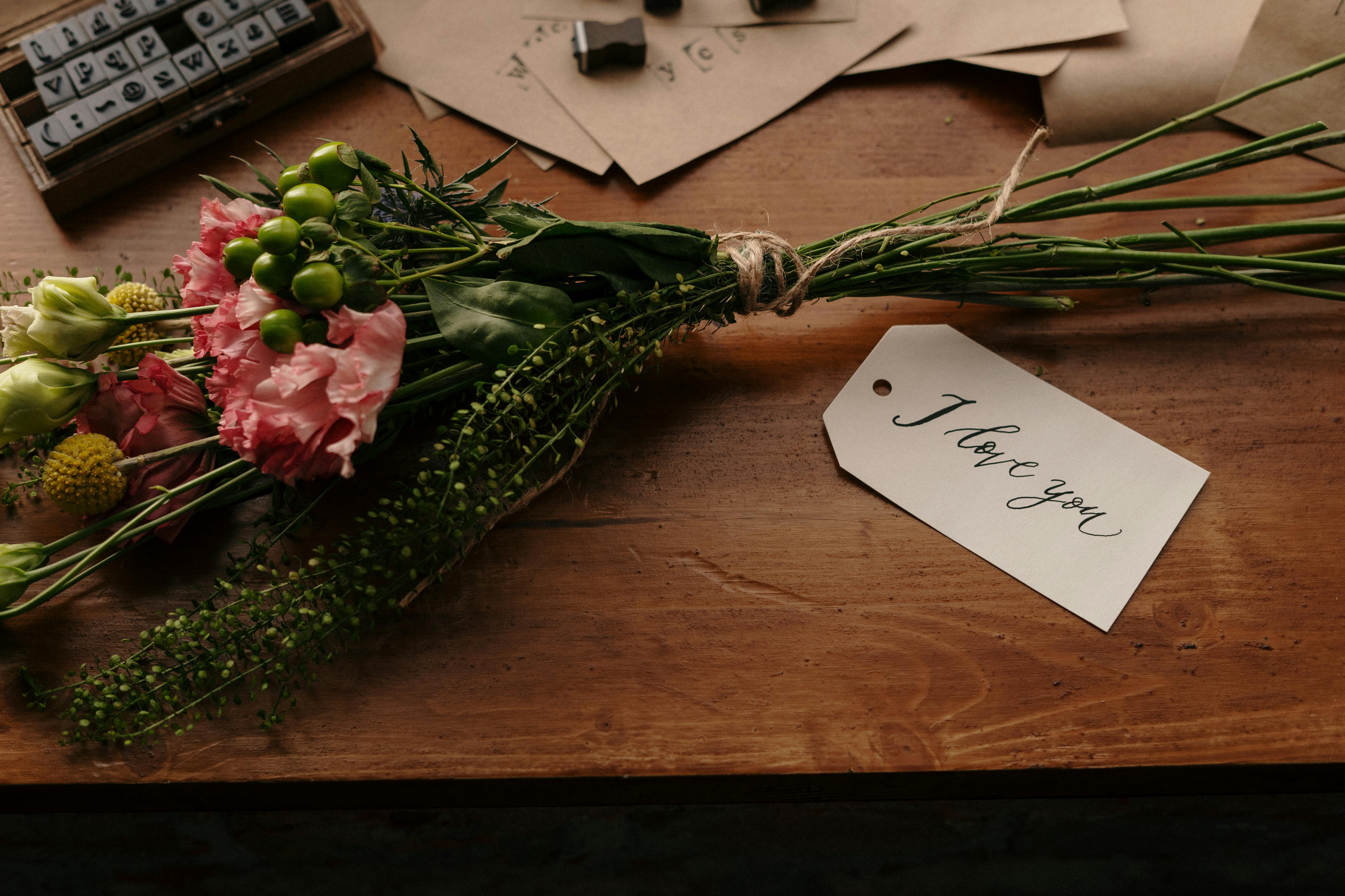 Bouquet of Flowers with Note Lying on Wooden Desk · Free Stock Photo