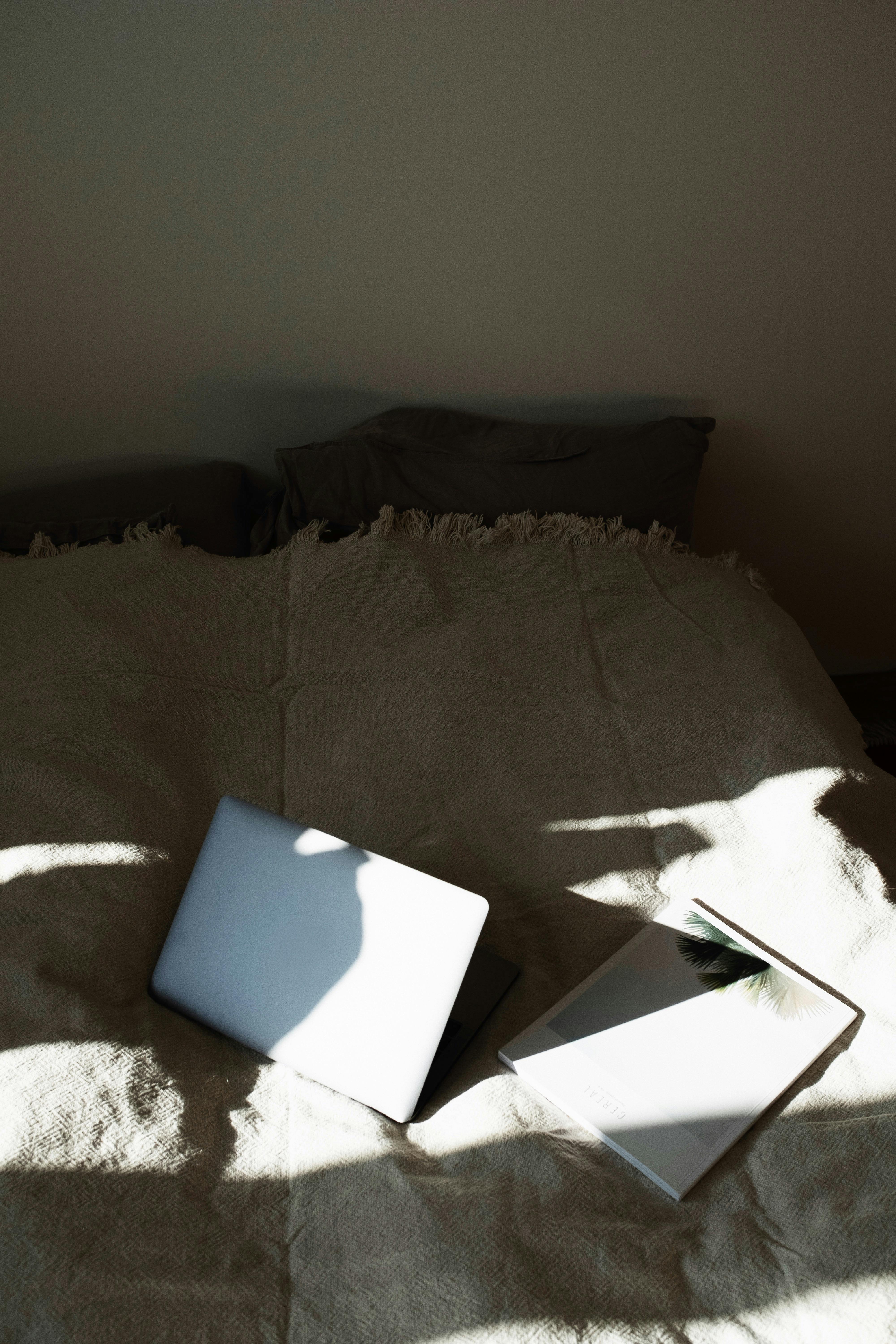 Laptop and book placed on blanket on bed in light bedroom · Free Stock ...