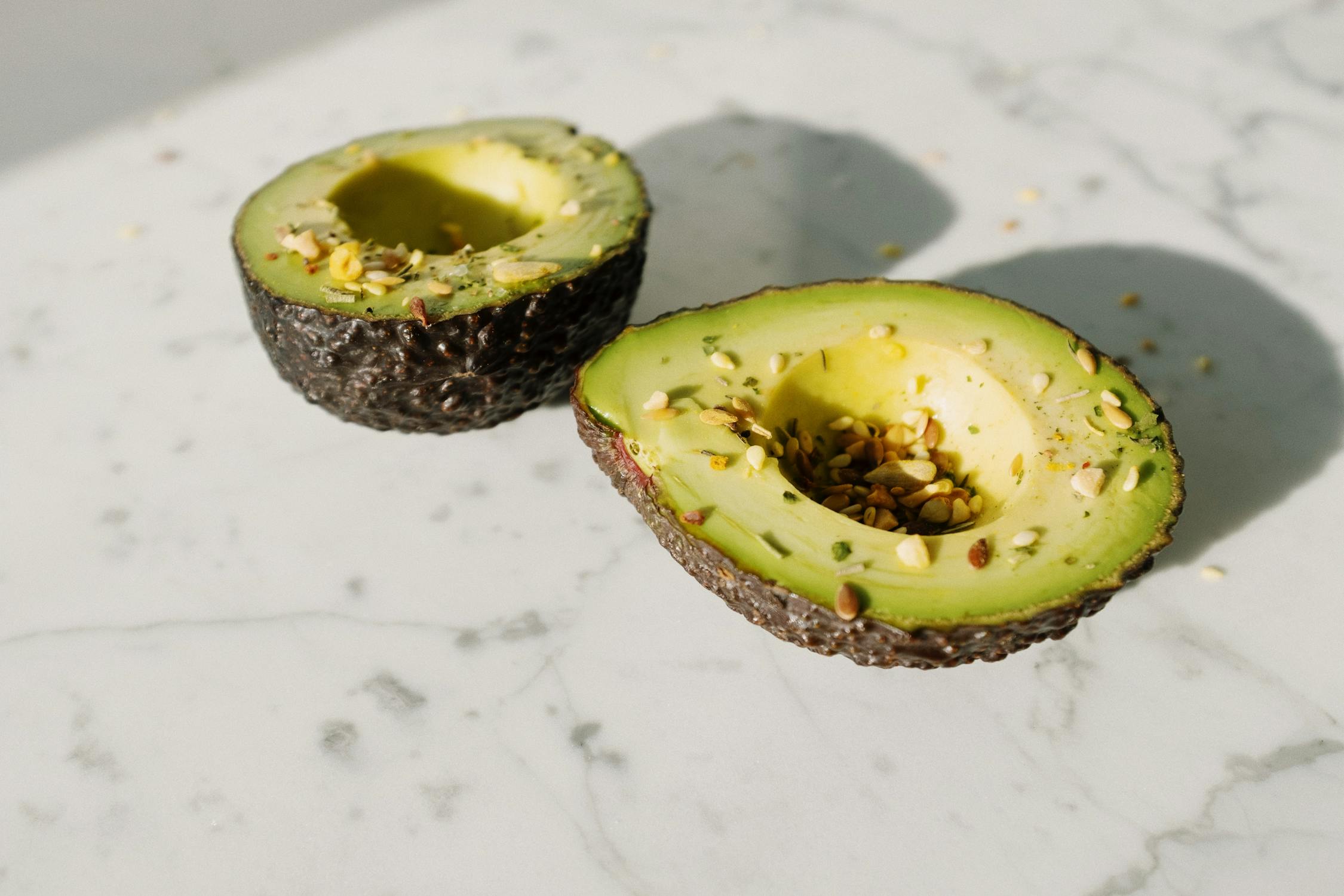 Yummy Halved Avocado With Various Seed Grains And On Marble Surface Yummy Halved Avocado With Various Seed Grains And On Marble Surface