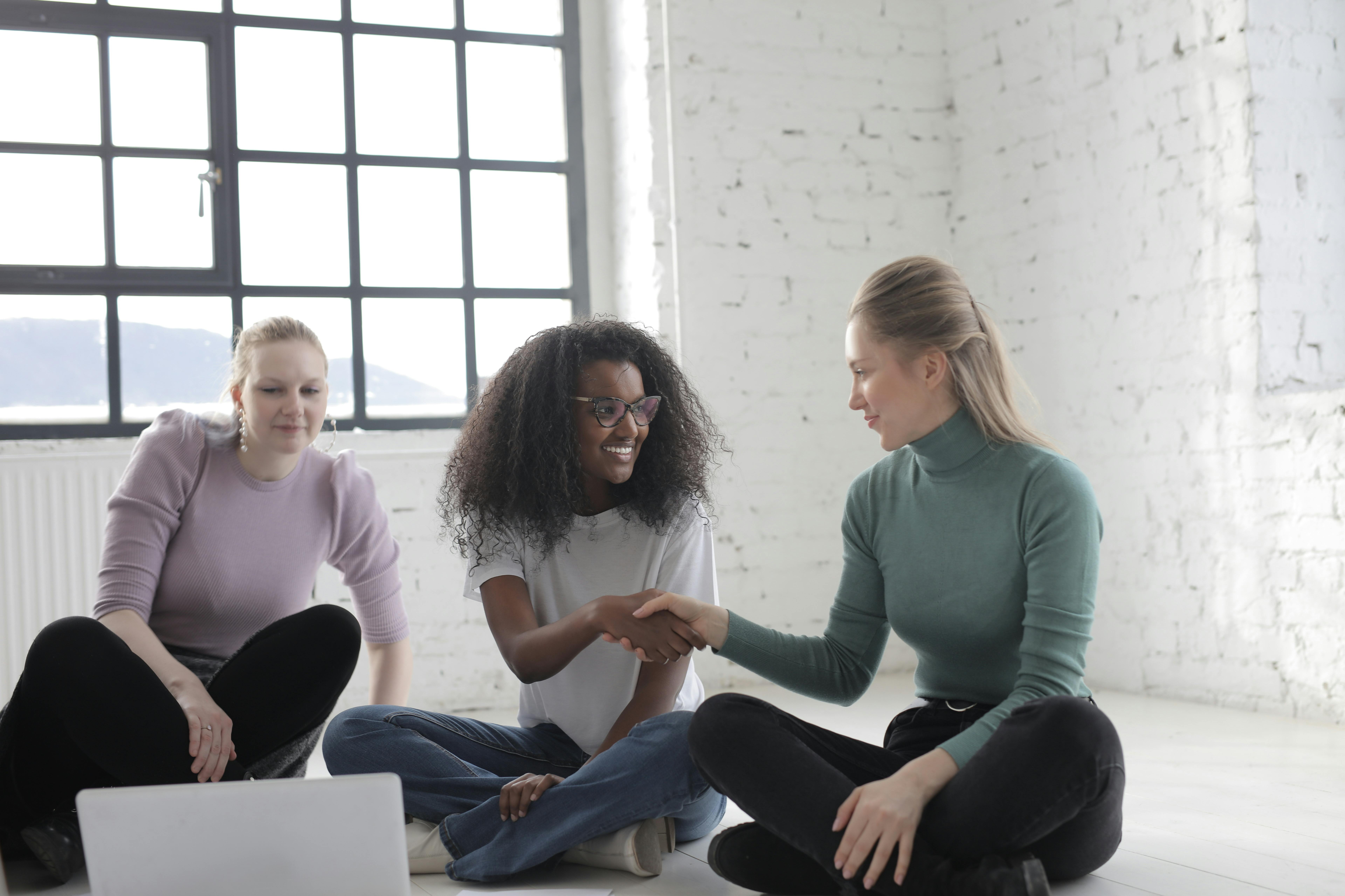 Diverse female colleagues shaking hands while sitting on floor · Free ...