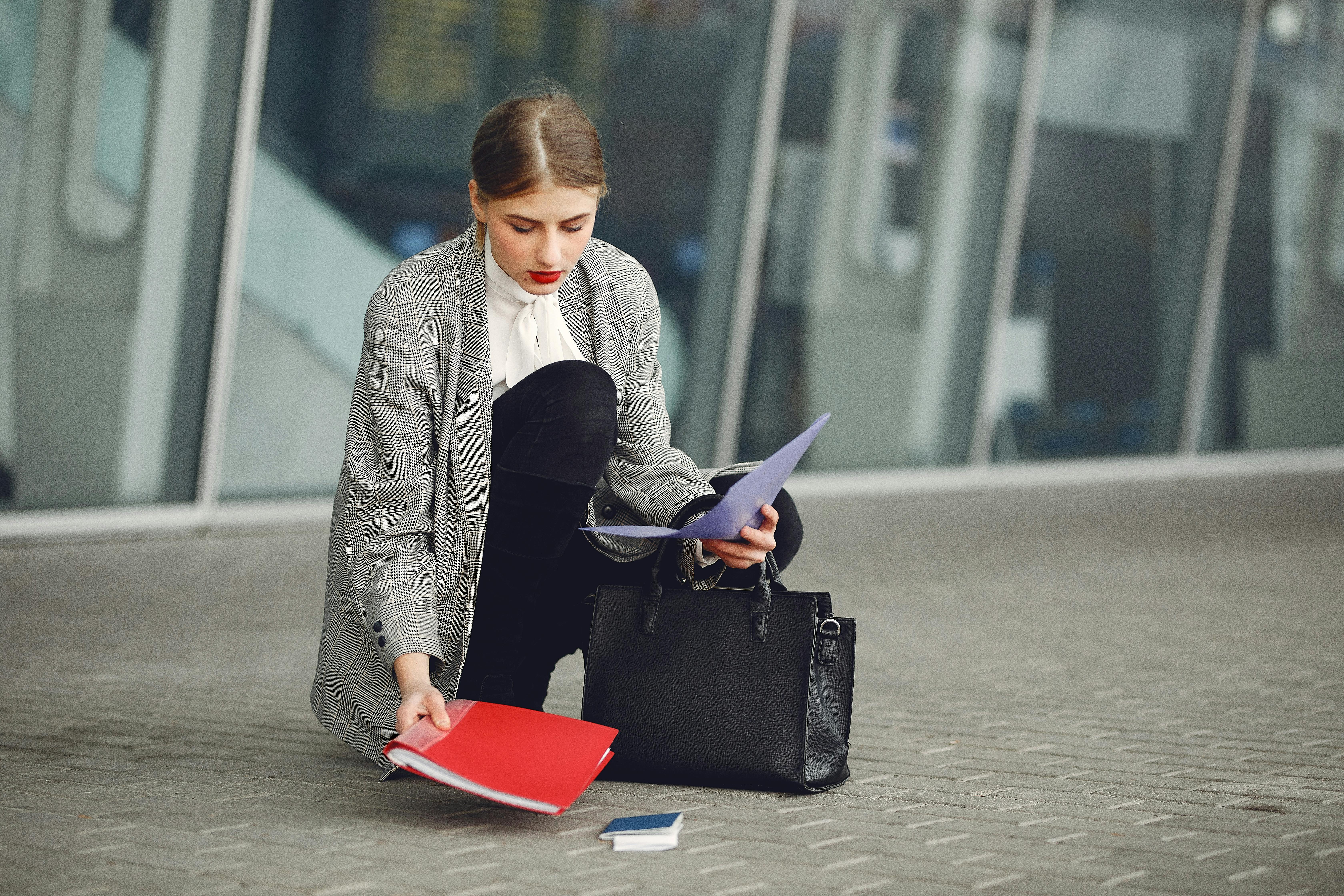 Serious young lady collecting documents from asphalt near airport ...