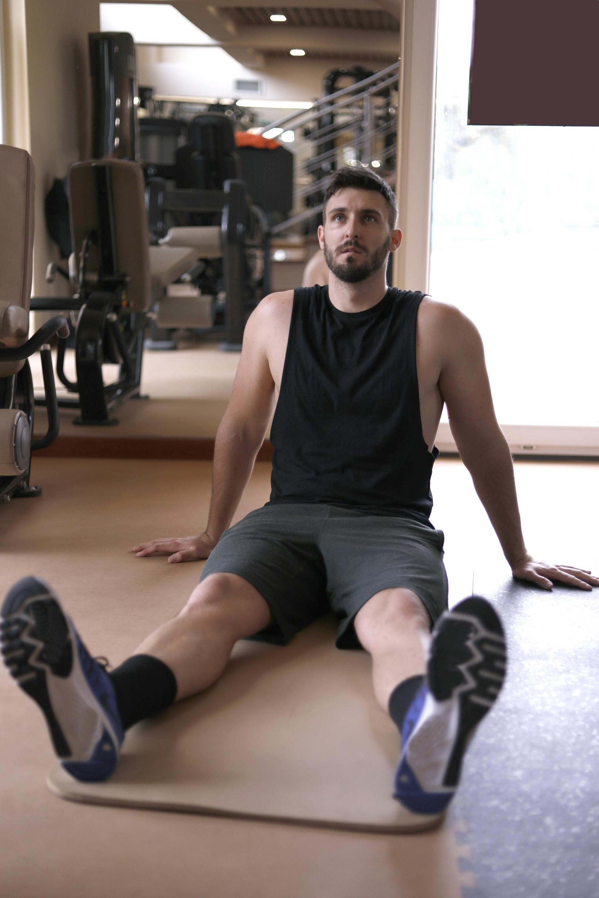 Serious young male athlete resting on mat during training in modern gym ...