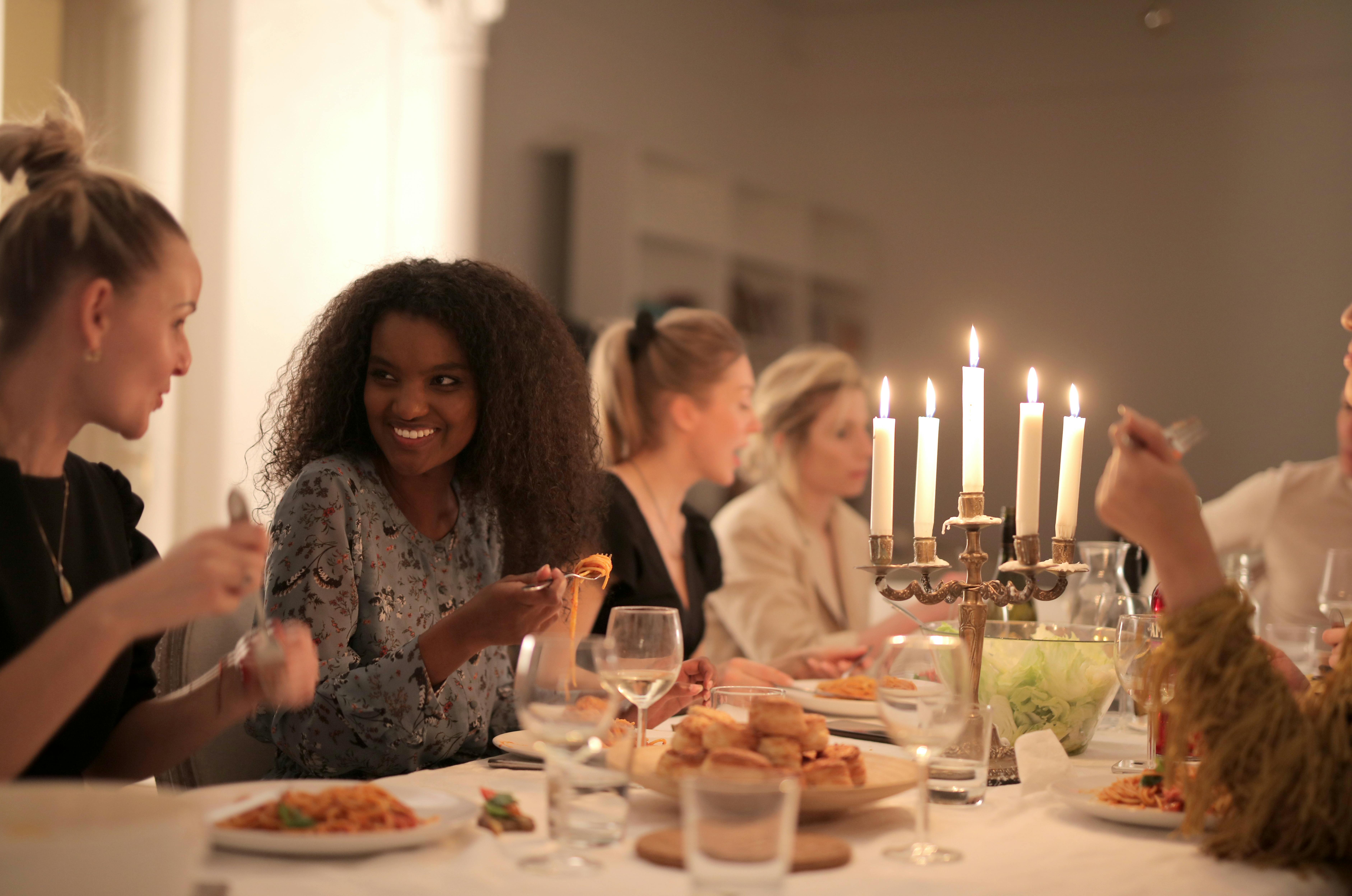 Group of People Sitting Around Table With Plates and Drinking Glasses ...