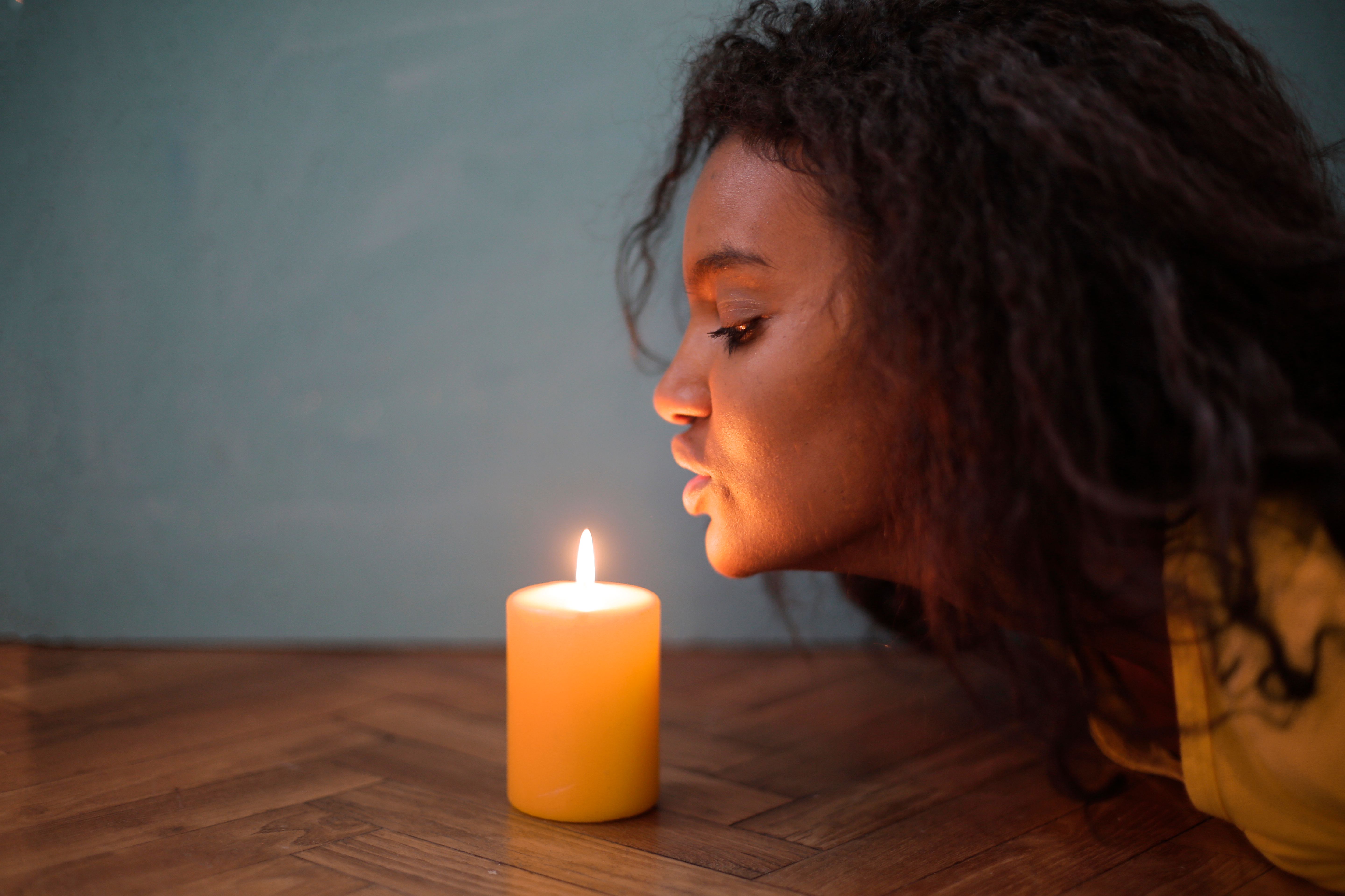 Young ethnic lady holding burning candle in hands near wall at home ...