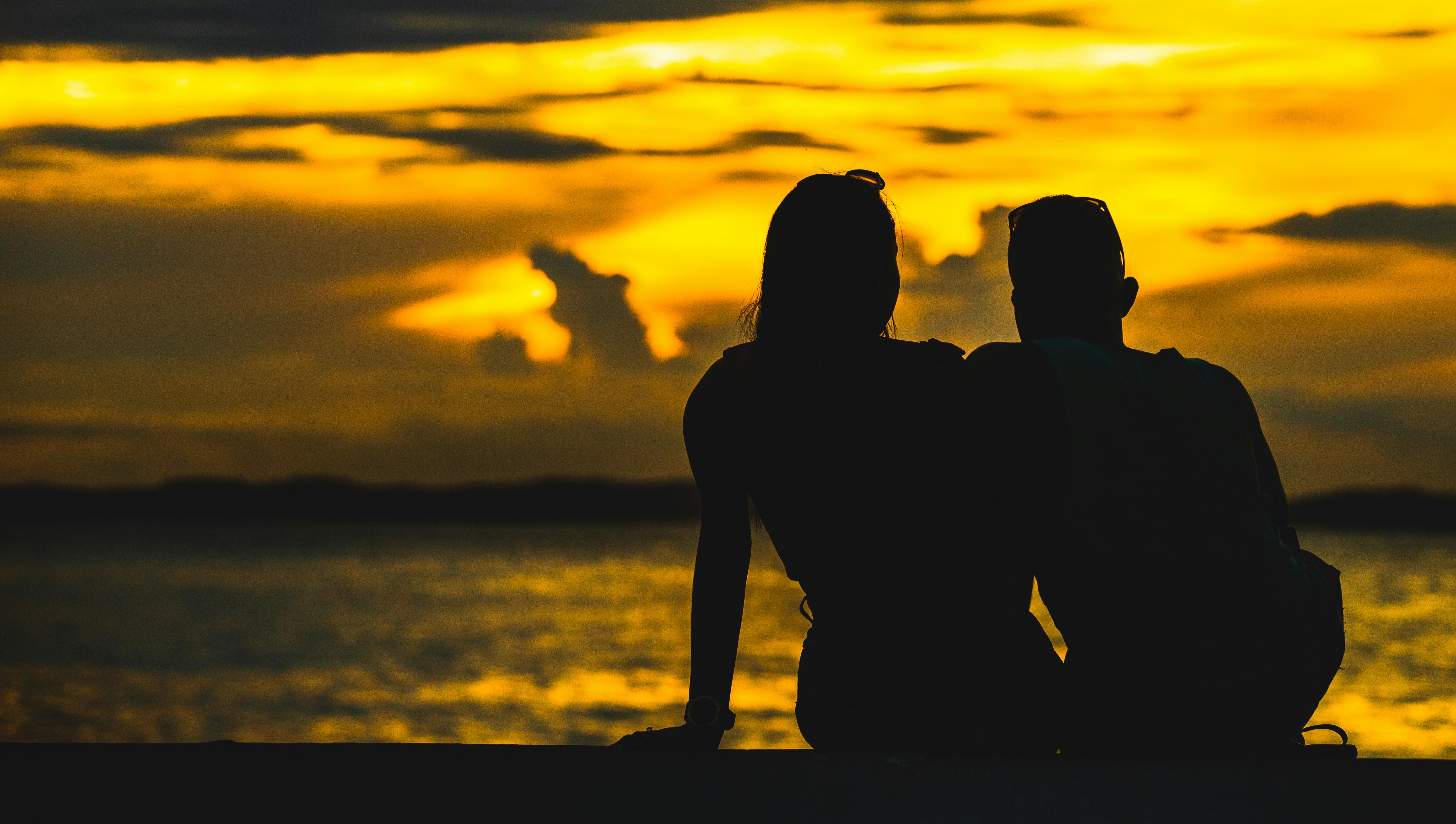 Silhouette of Couple Sitting on Seashore during Sunset · Free Stock Photo