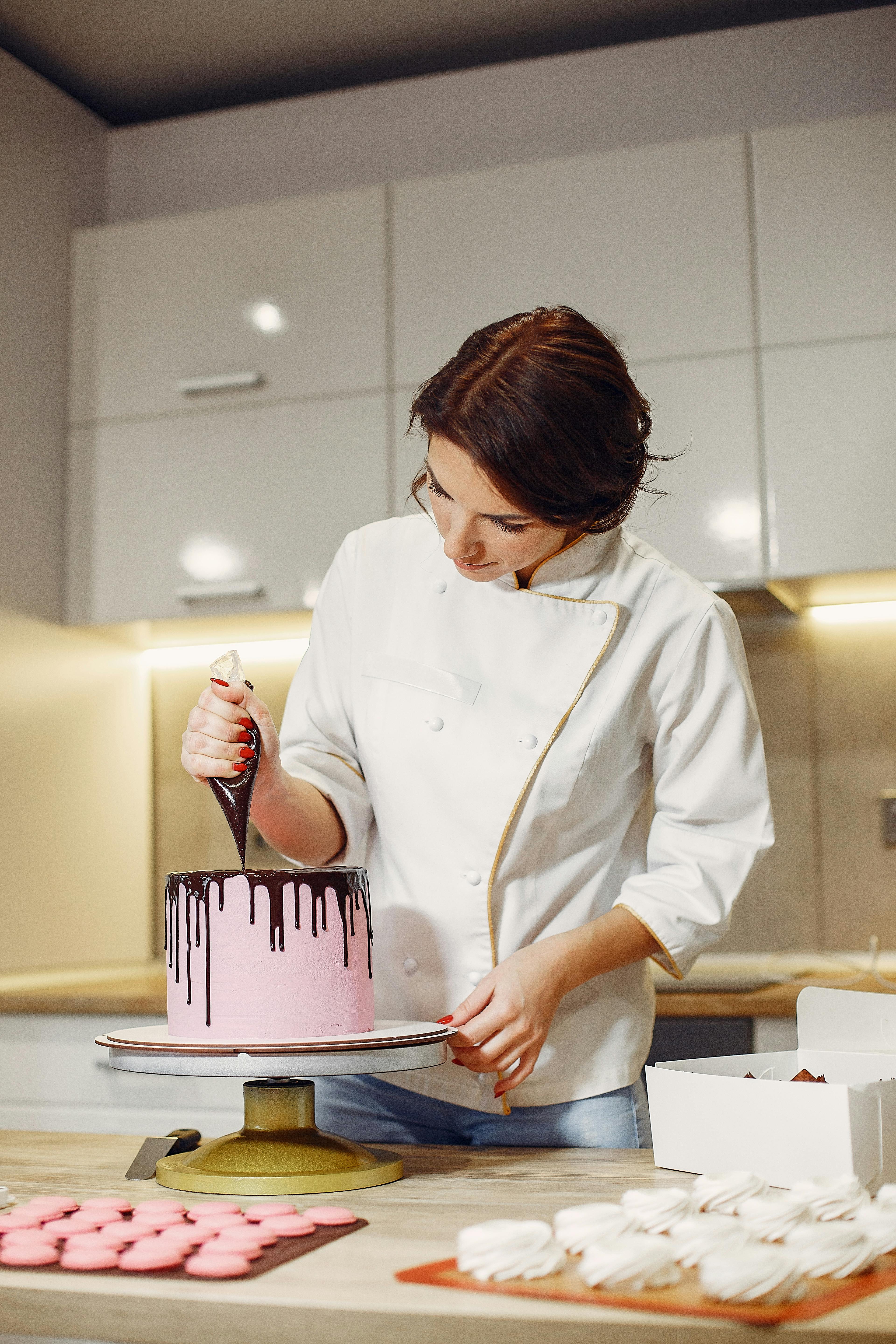 Focused female pastry chef preparing cake and desserts with smartphone ...