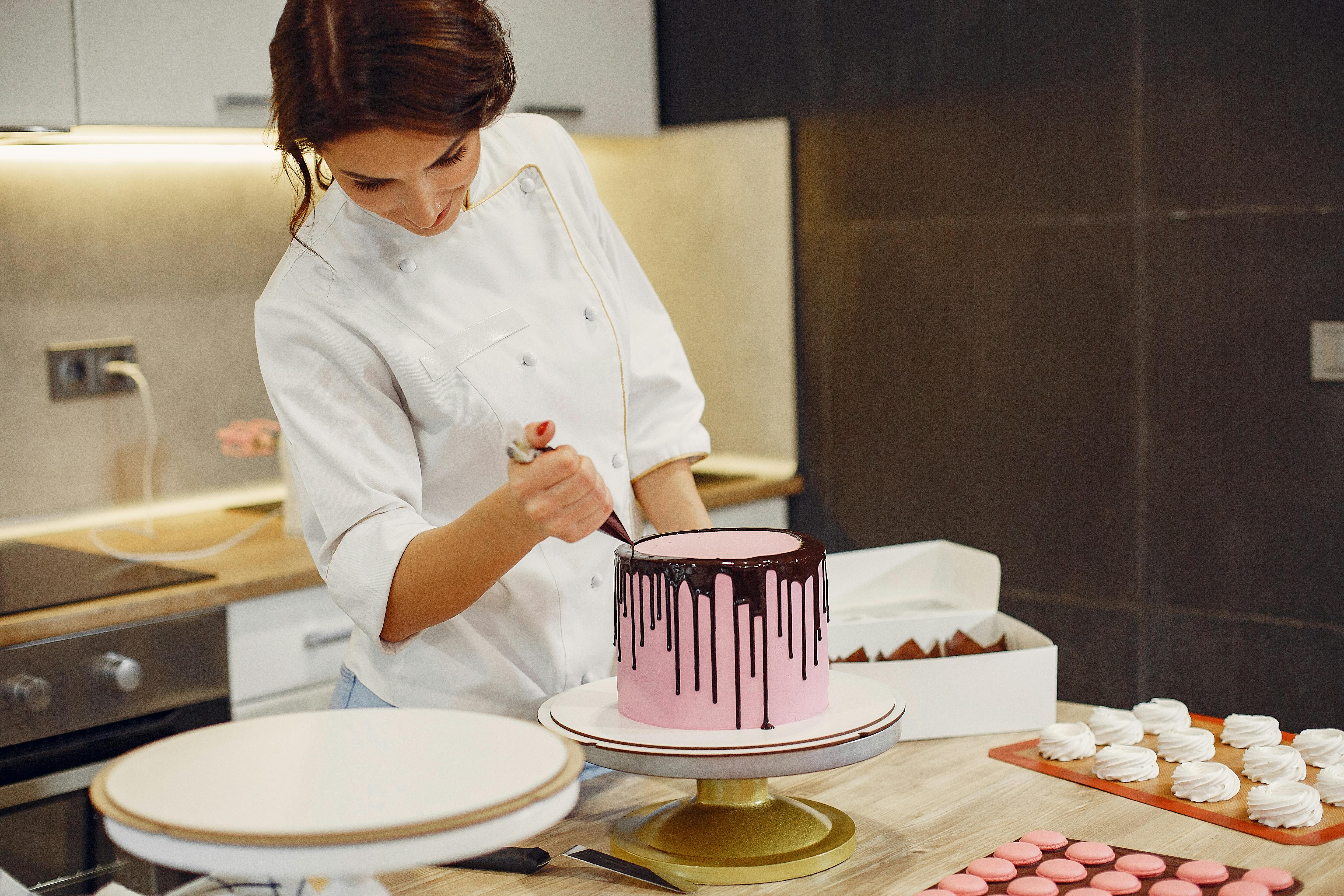 Smiling young woman squeezing chocolate from pastry bag on cake in ...