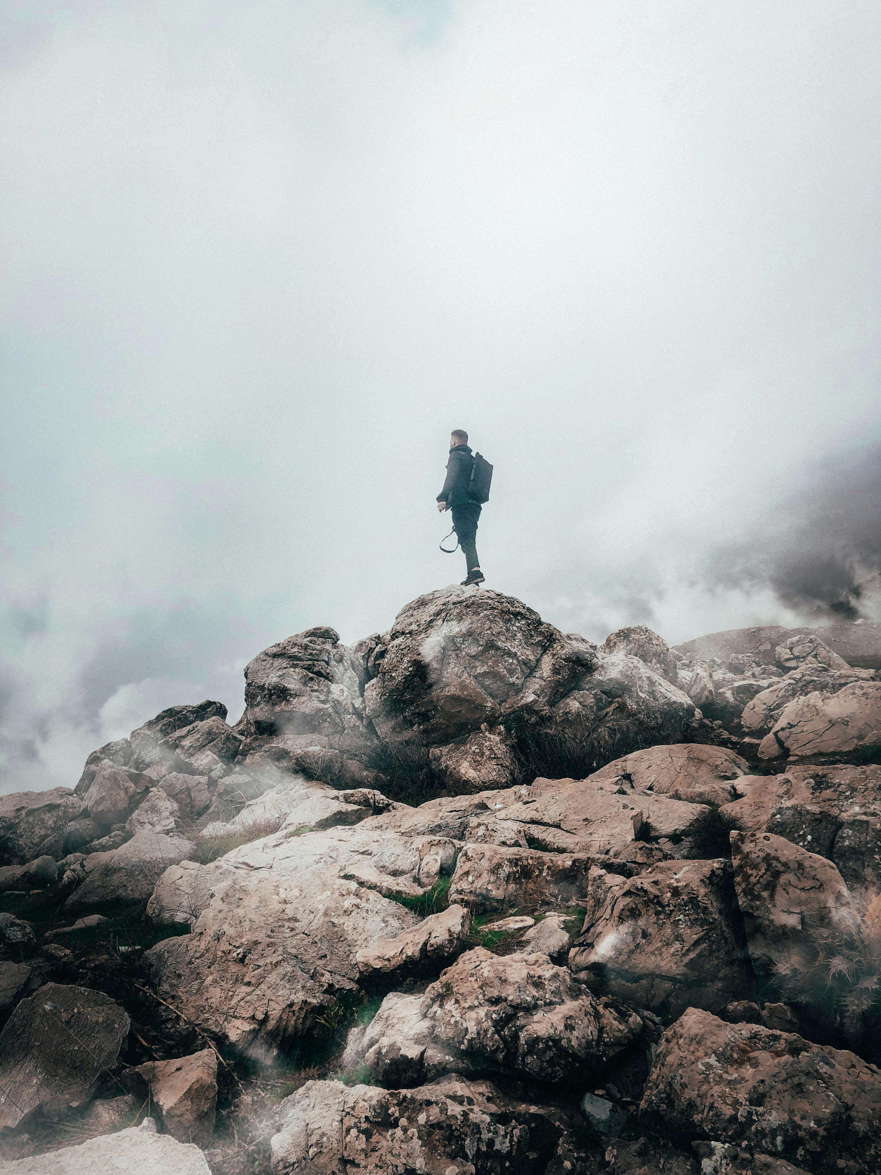 Man in Black Jacket Standing on Brown Rock Formation Under White Clouds ...